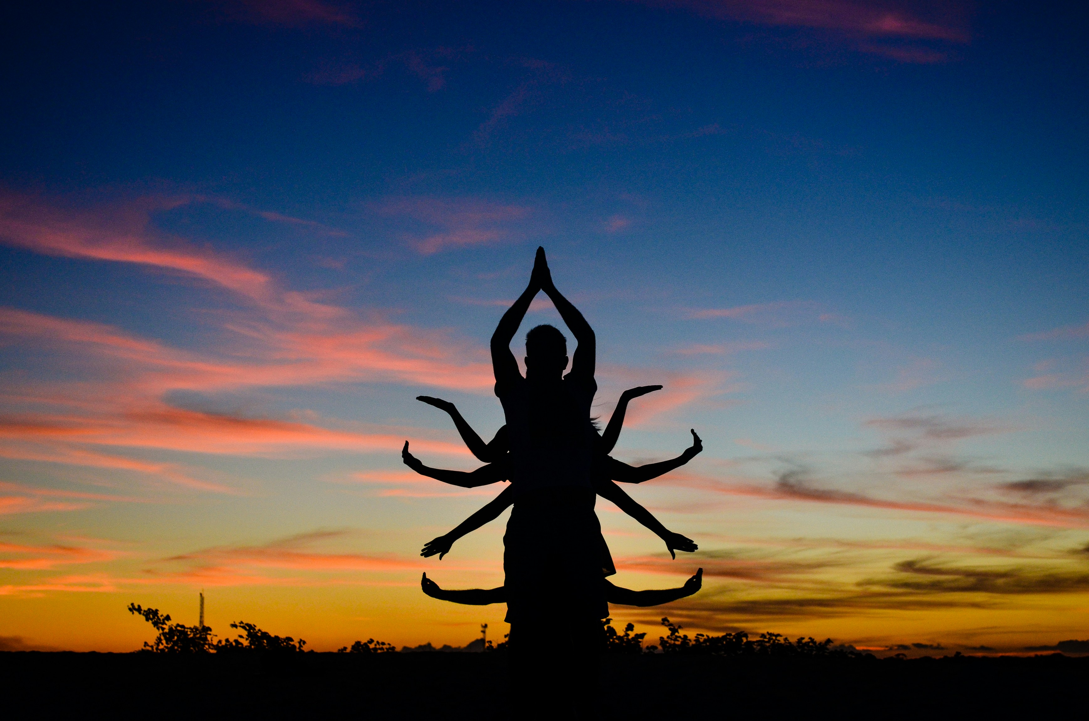 Silhouette of a multi-armed figure against a vivid sunset sky.