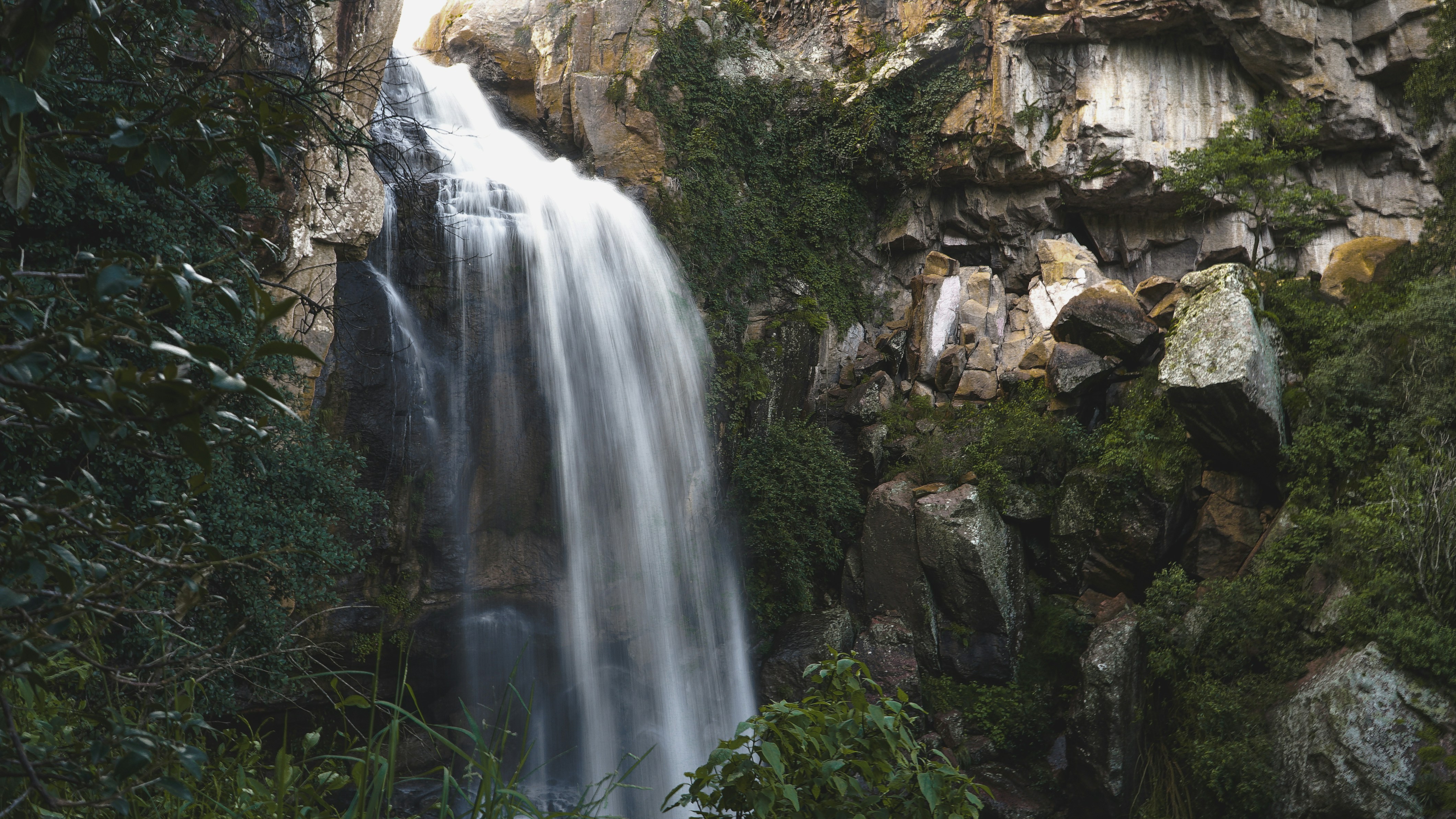 Majestic waterfall cascading over rocky cliffs, surrounded by lush greenery and moss-covered stones.