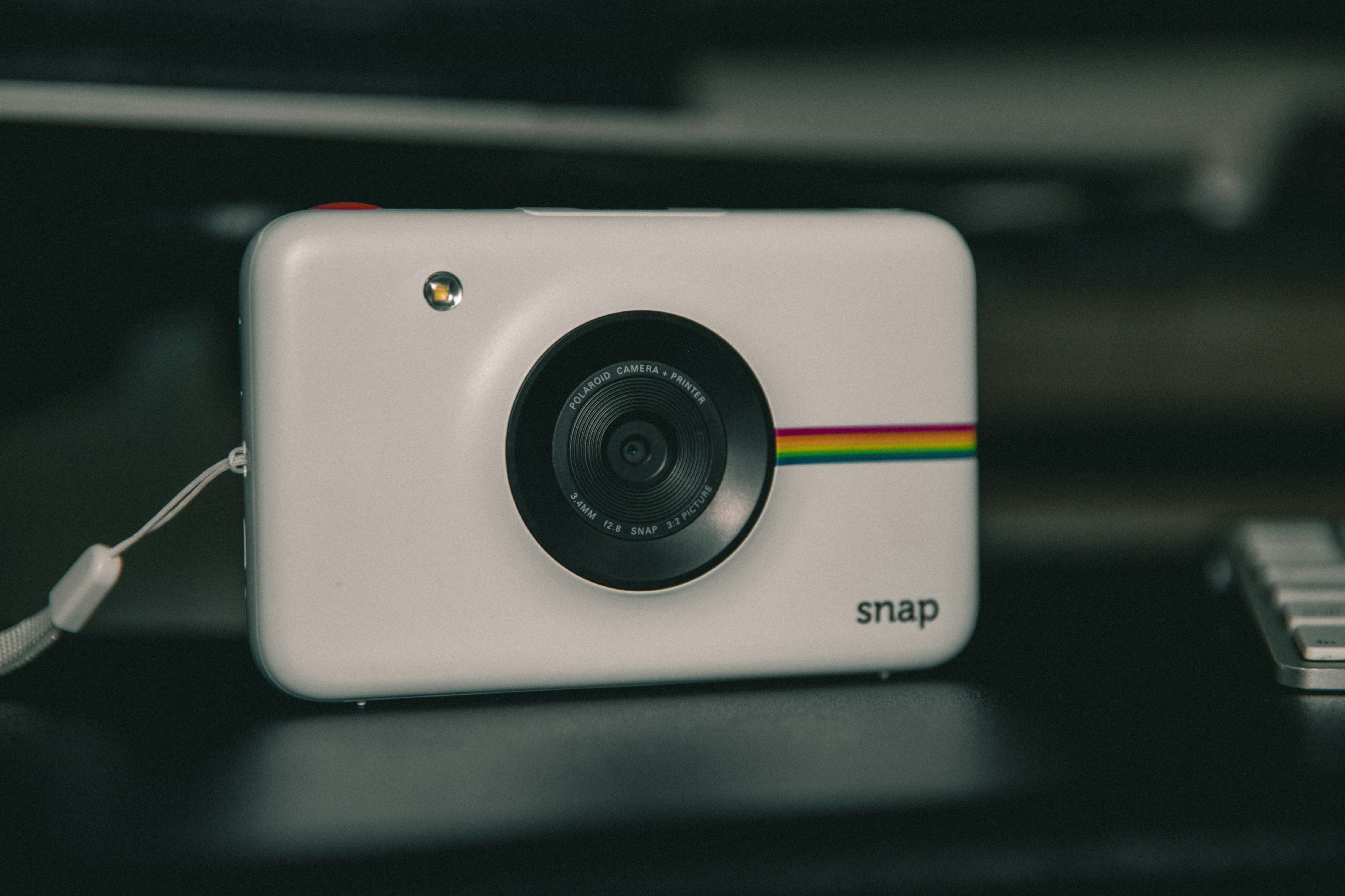 Minimalist white Snap camera resting on a dark desk with a subtle rainbow stripe