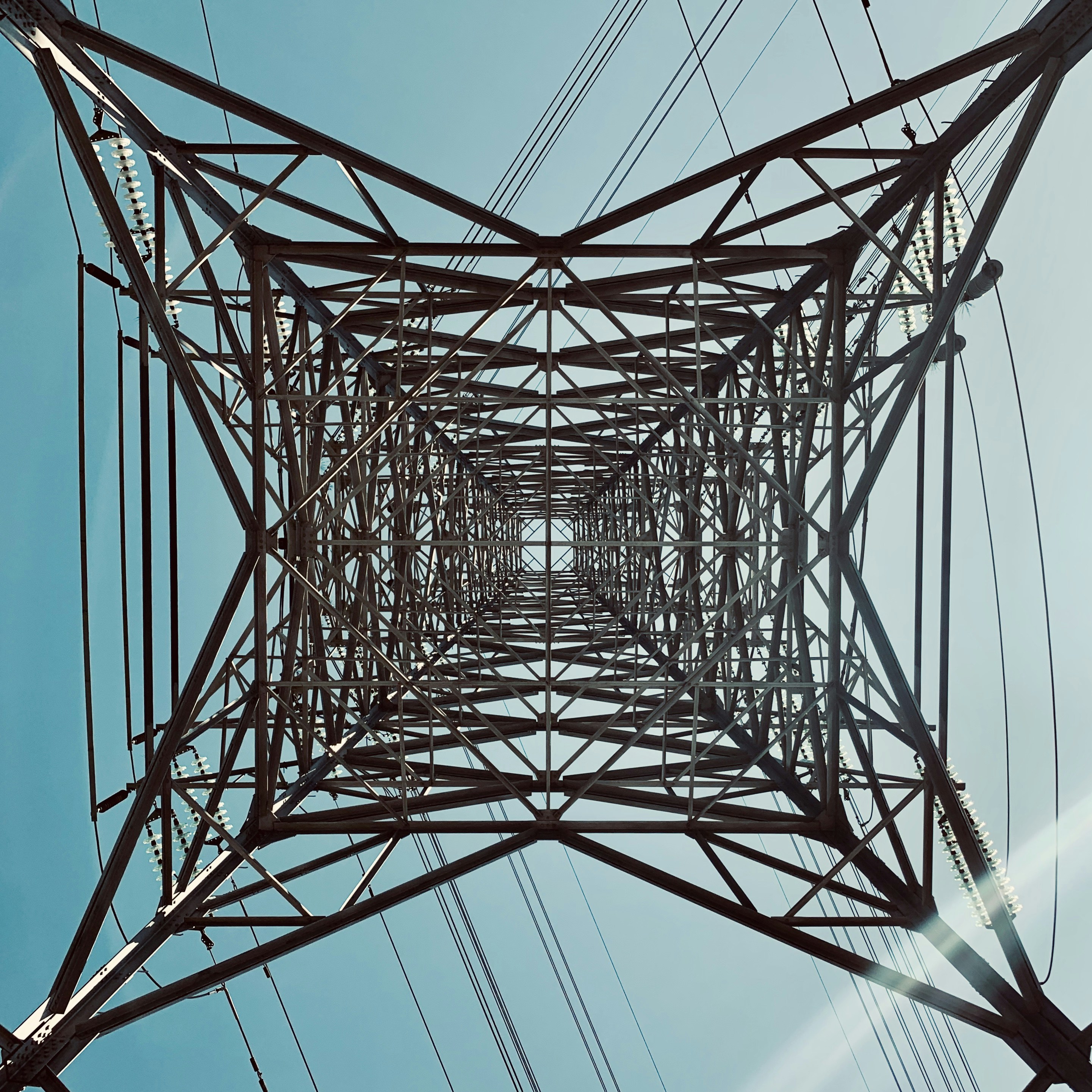 Intricate lattice of a power tower viewed from below against a clear blue sky.