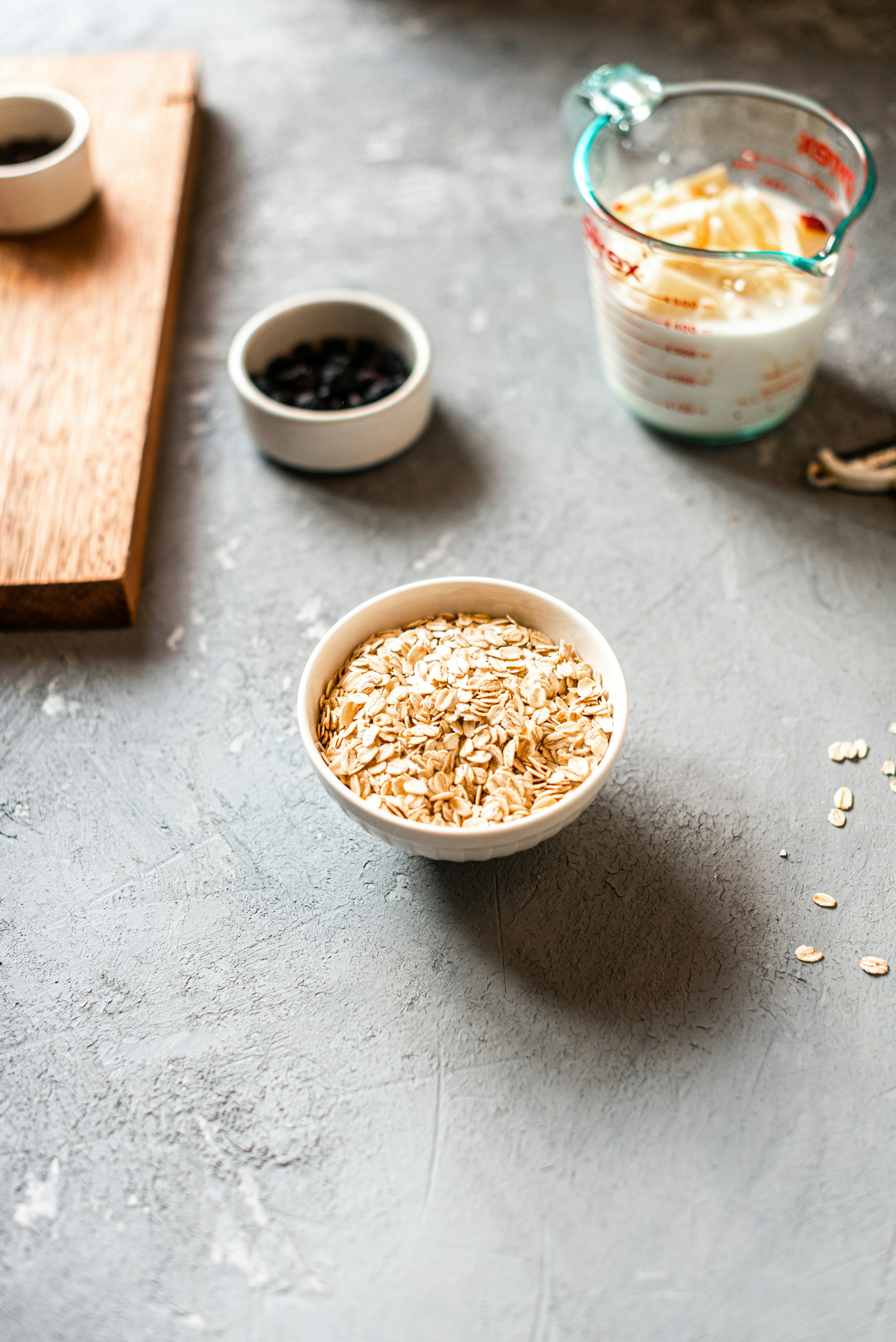 A bowl of rolled oats sits on a textured surface, surrounded by measuring cups and ingredients for a wholesome breakfast.