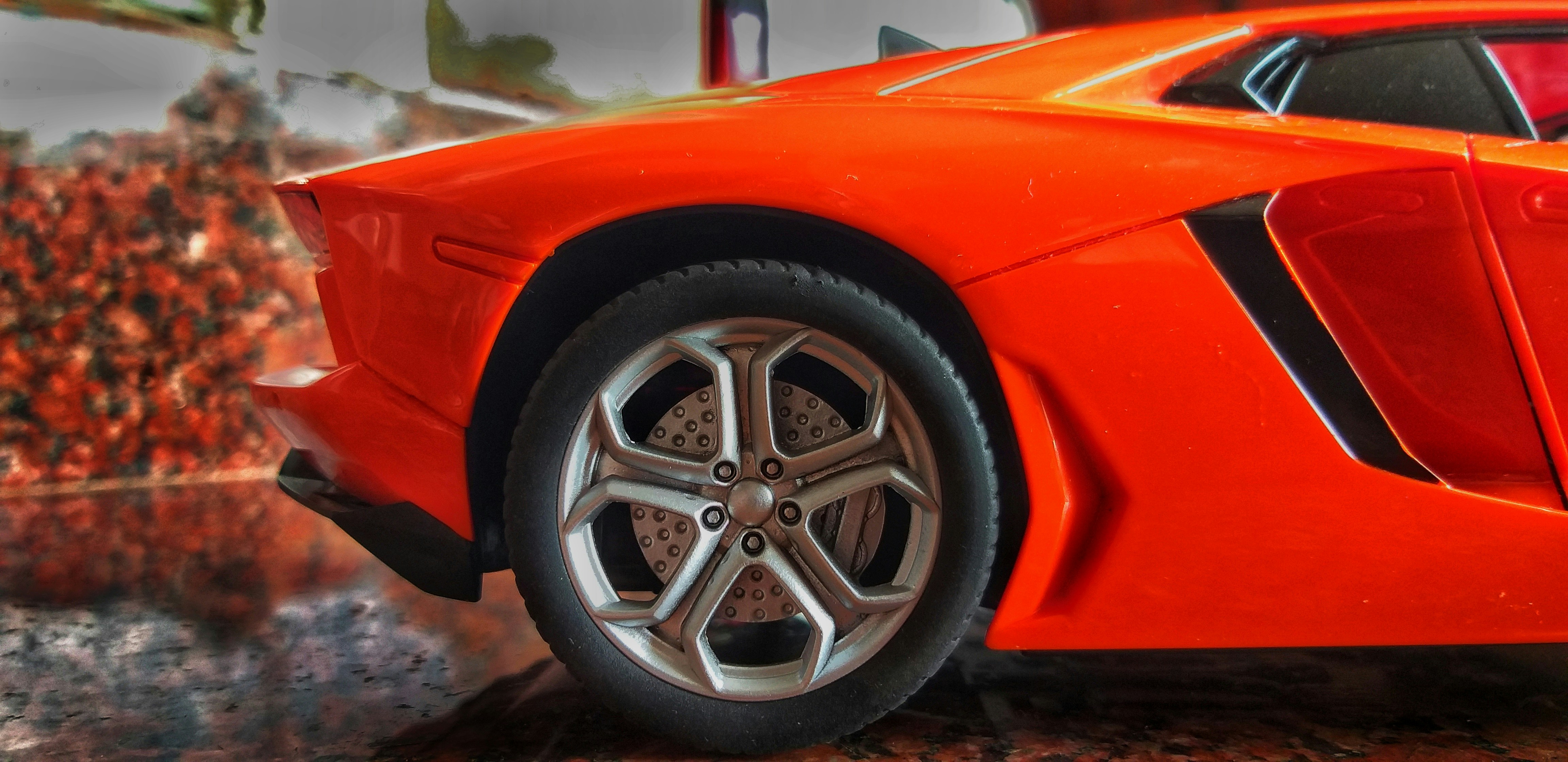 Close-up of an orange sports car model showcasing intricate wheel design and body contours.