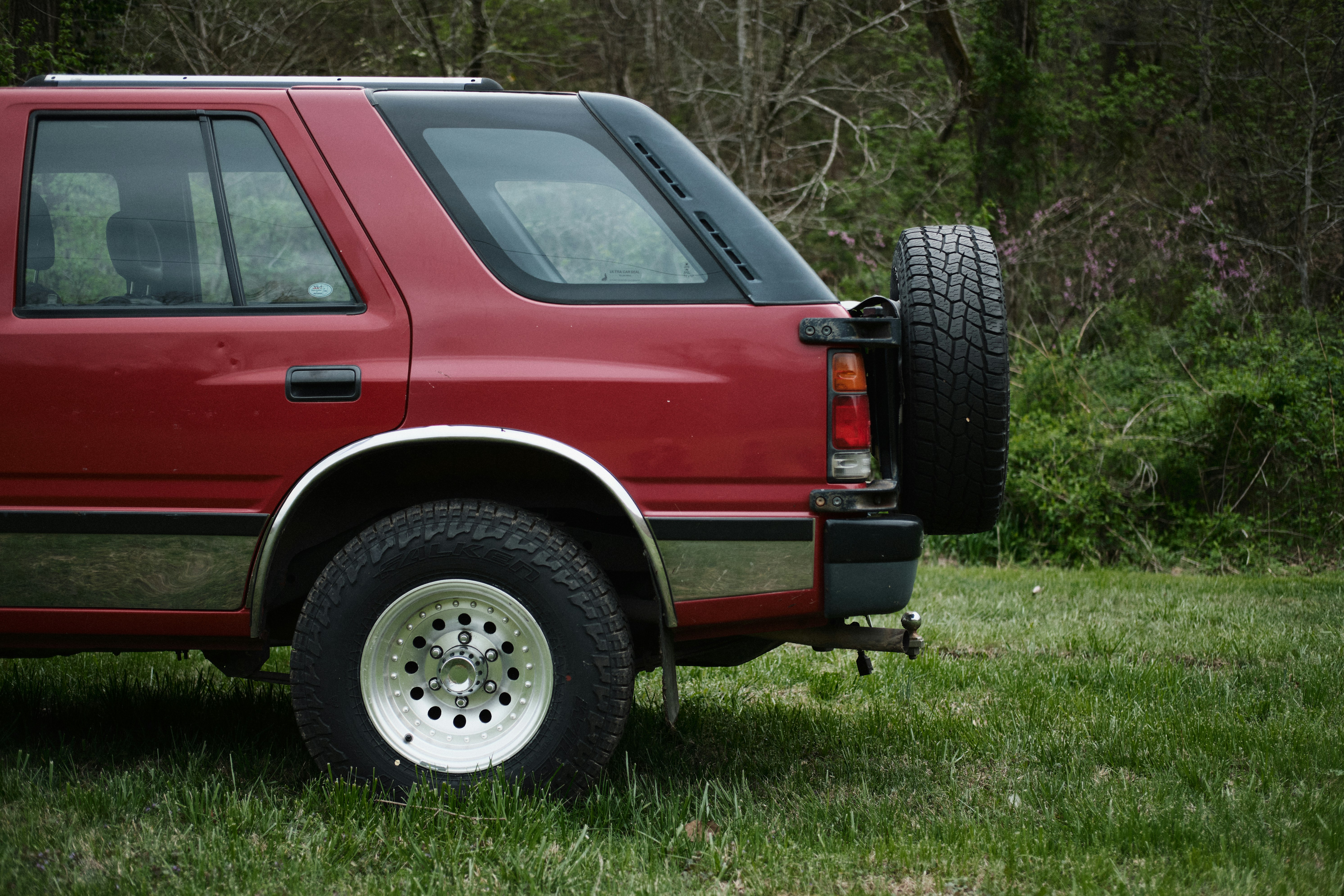 Rear-Quarter View of a Red SUV with Spare Tire in a grassy Field