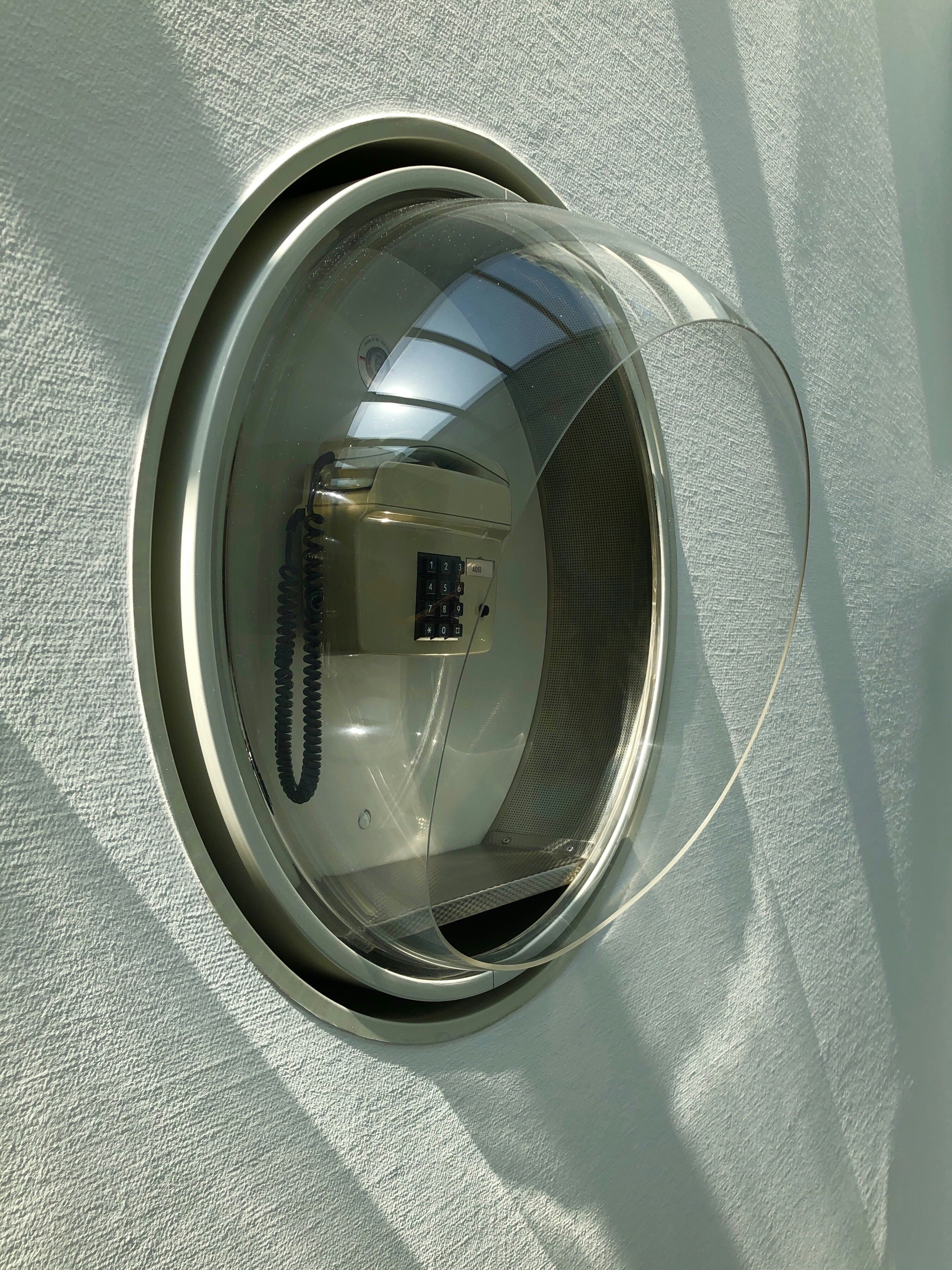 Porthole Intercom: A Sunlit Round Window Framing a Vintage Device