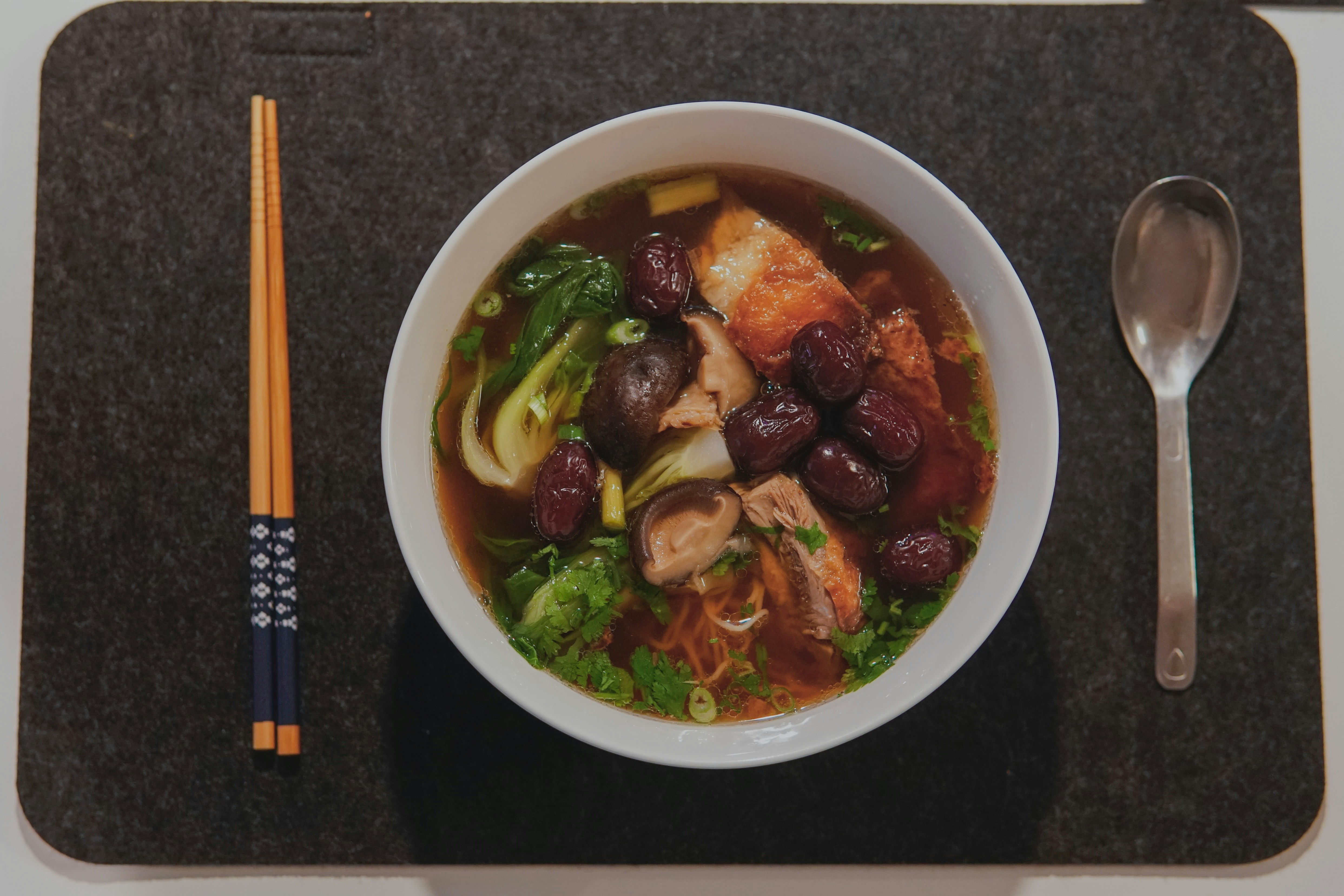 Umami Orbit: A Bowl of Greens, Mushrooms, and Rich Broth on a Dark Placemat