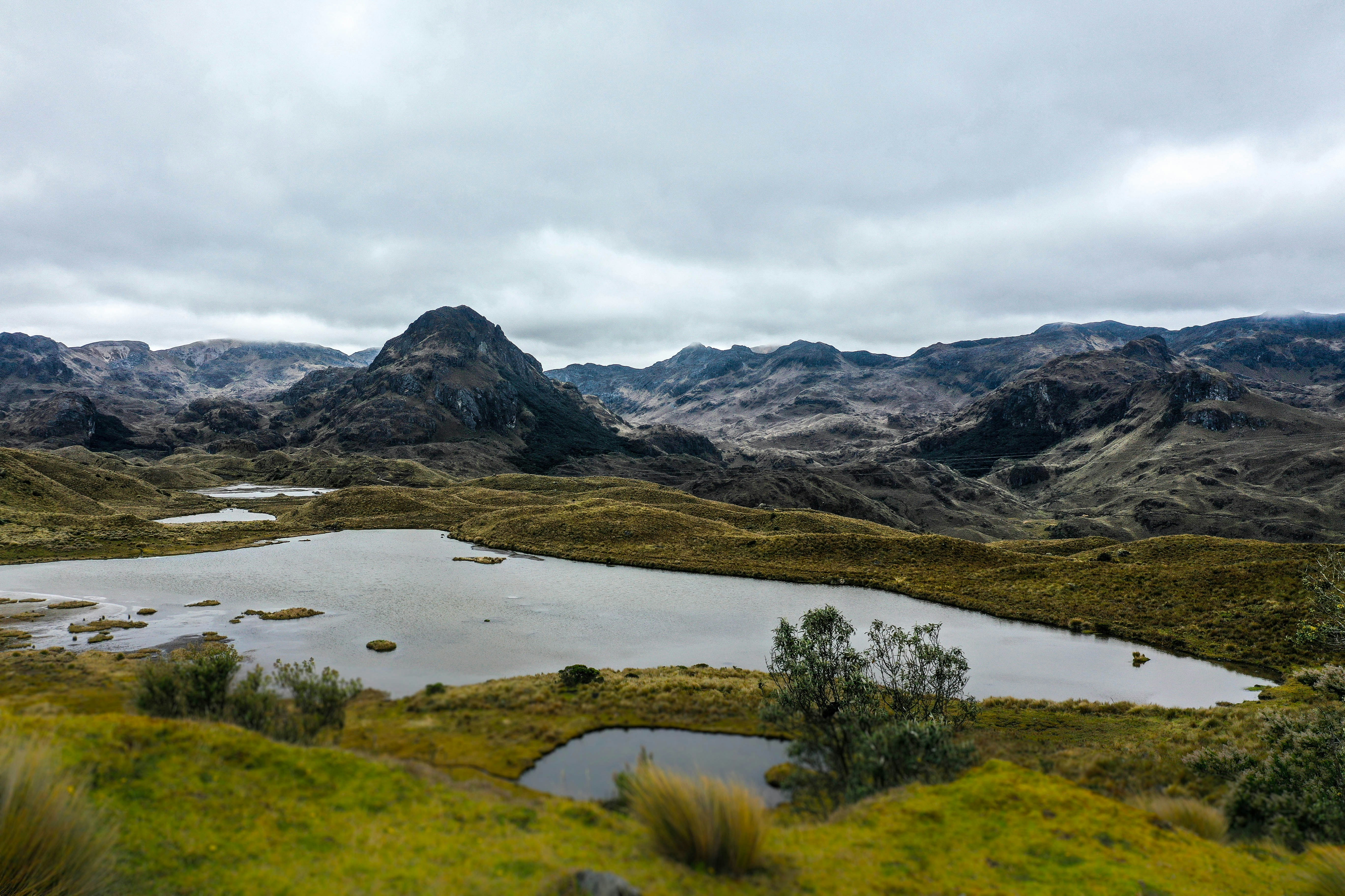Vast highland landscape with rugged hills and a tranquil lake under a cloudy sky.