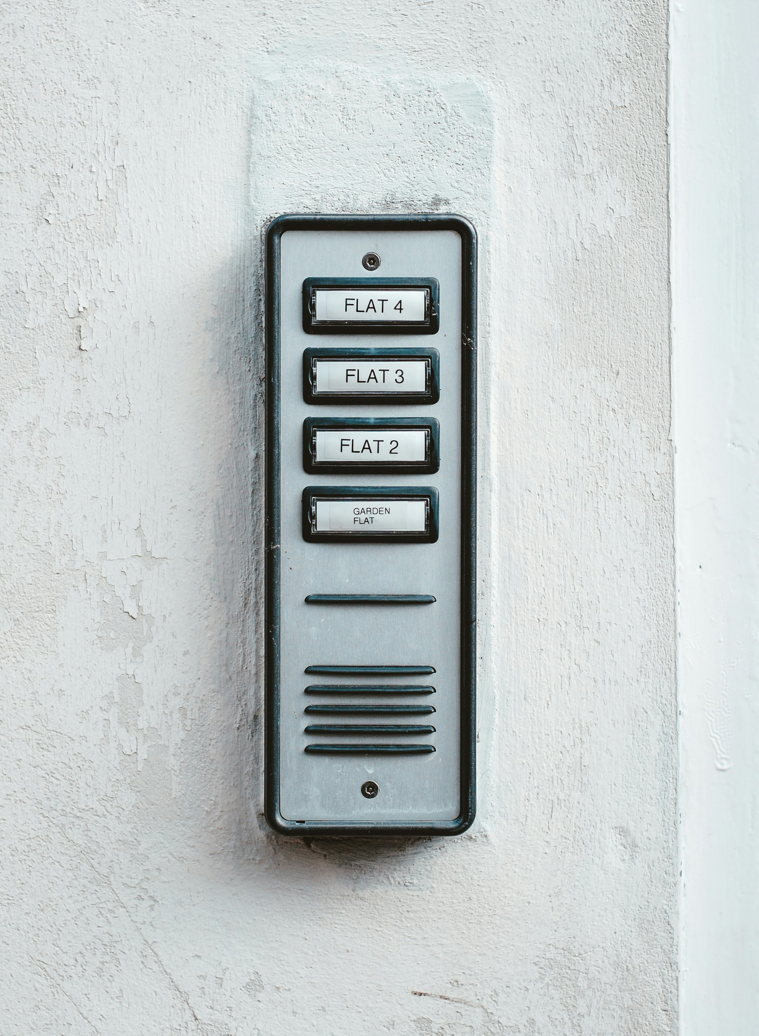 Intercom panel with buttons labeled for different flats, mounted on a textured wall. A functional piece for communication in a shared living space.