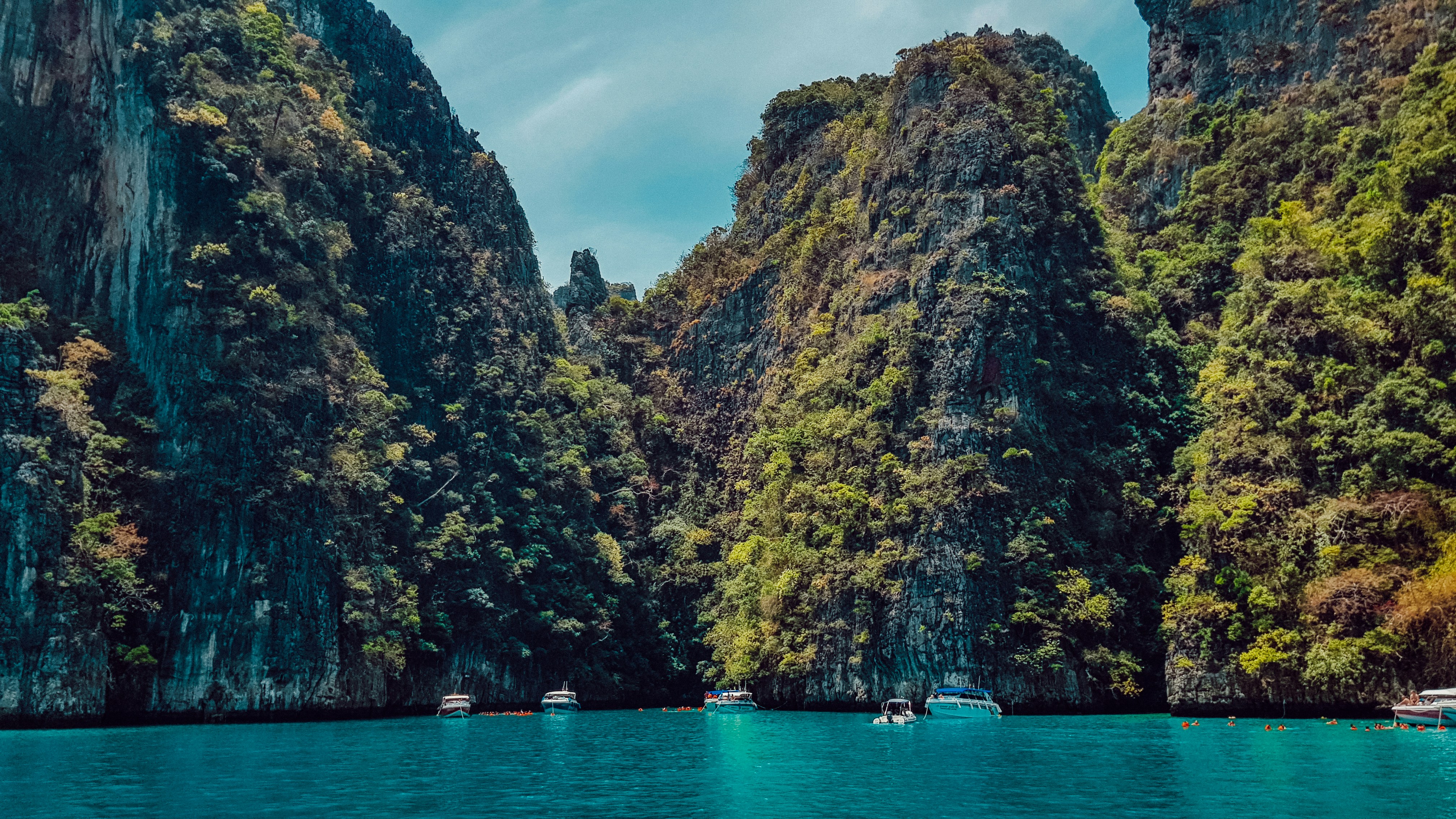 Lush green cliffs rise dramatically from turquoise waters, with boats gently floating in the serene bay. A tranquil scene capturing the harmony of nature.
