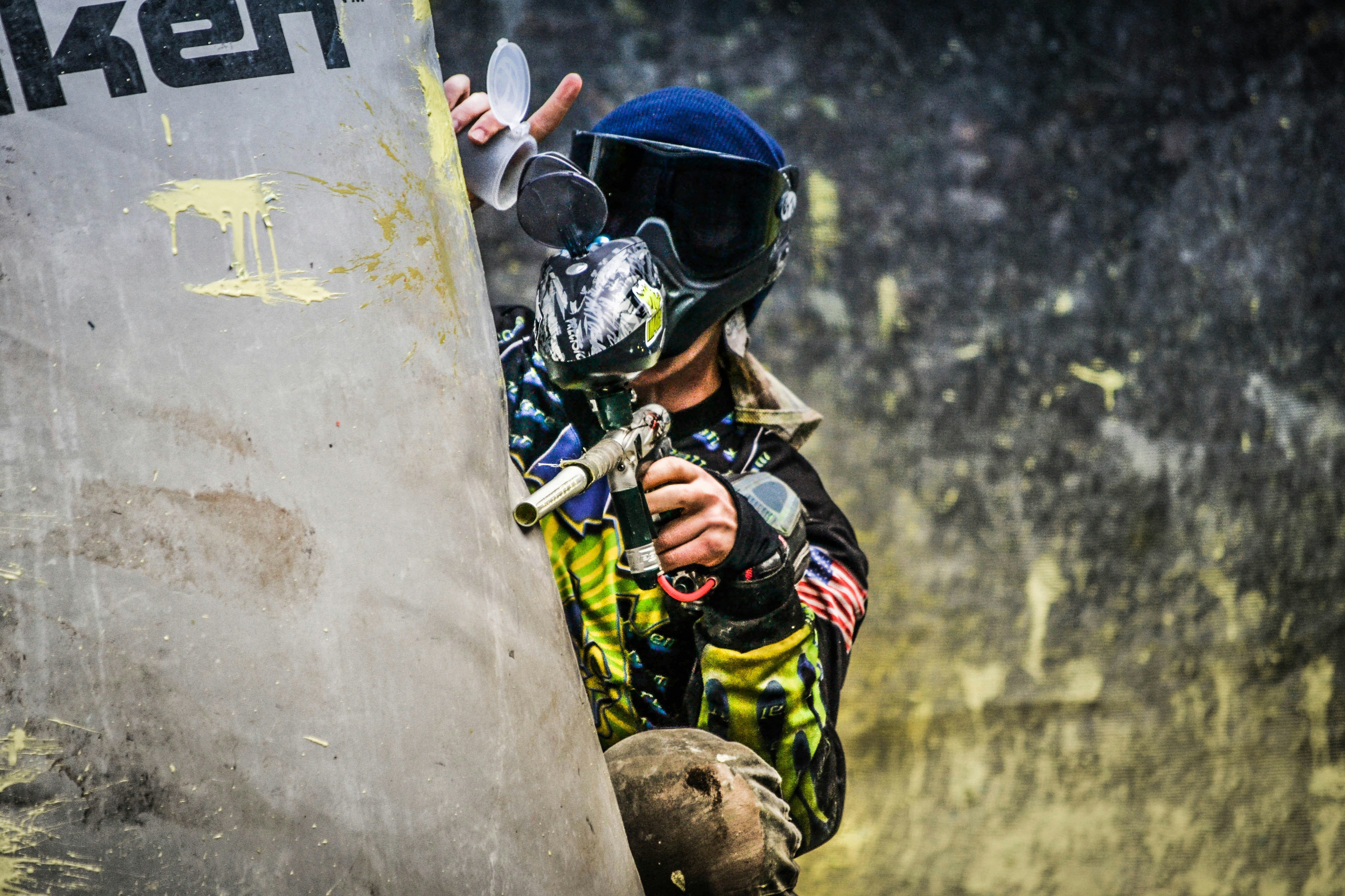 Paintball player in vibrant gear aiming from behind a barrier.