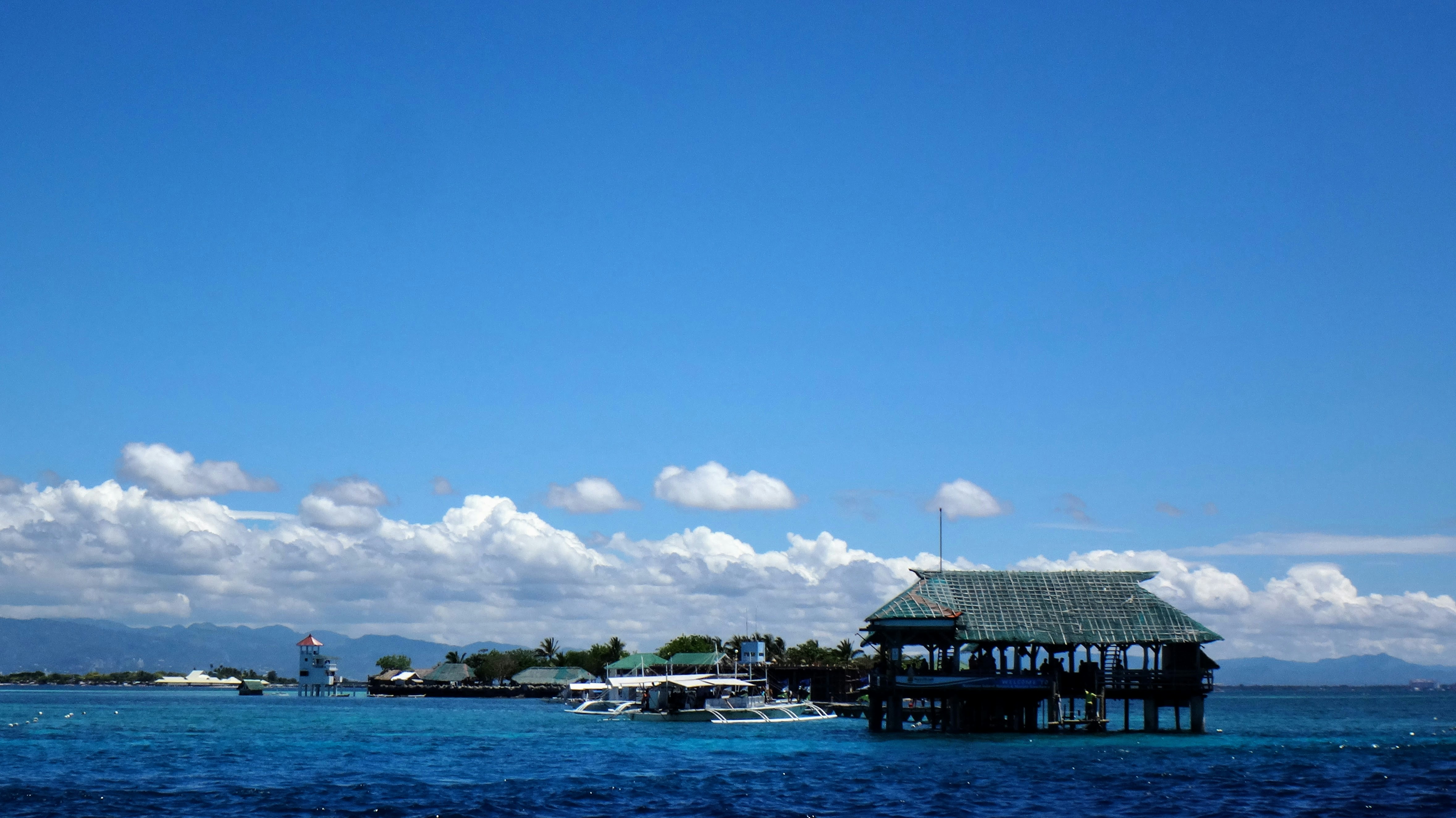 Floating hut on a vibrant blue sea under a clear sky with distant mountains.