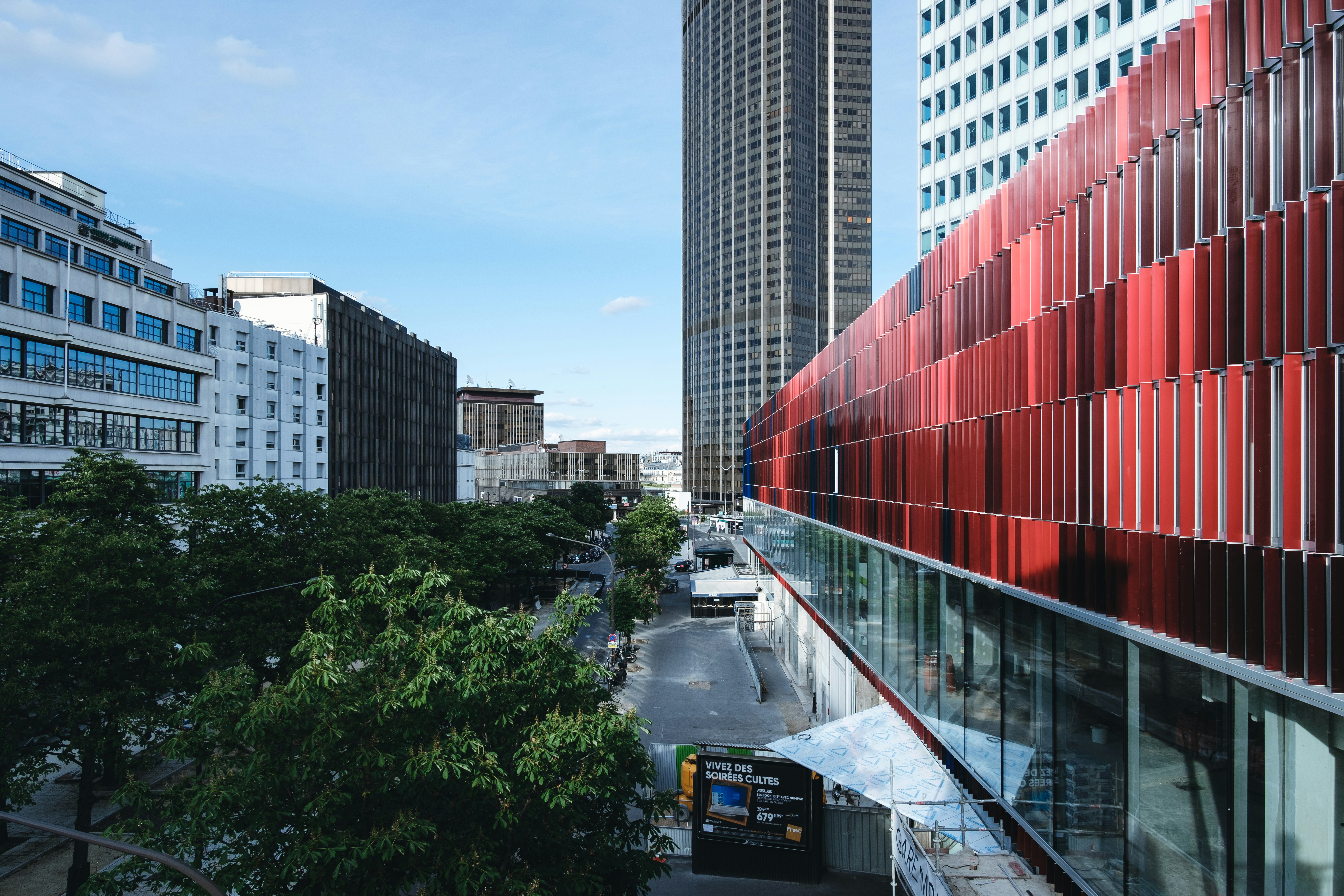 Modern architectural structures juxtaposed against lush greenery, showcasing a vibrant cityscape. The red facade reflects contemporary design elements.