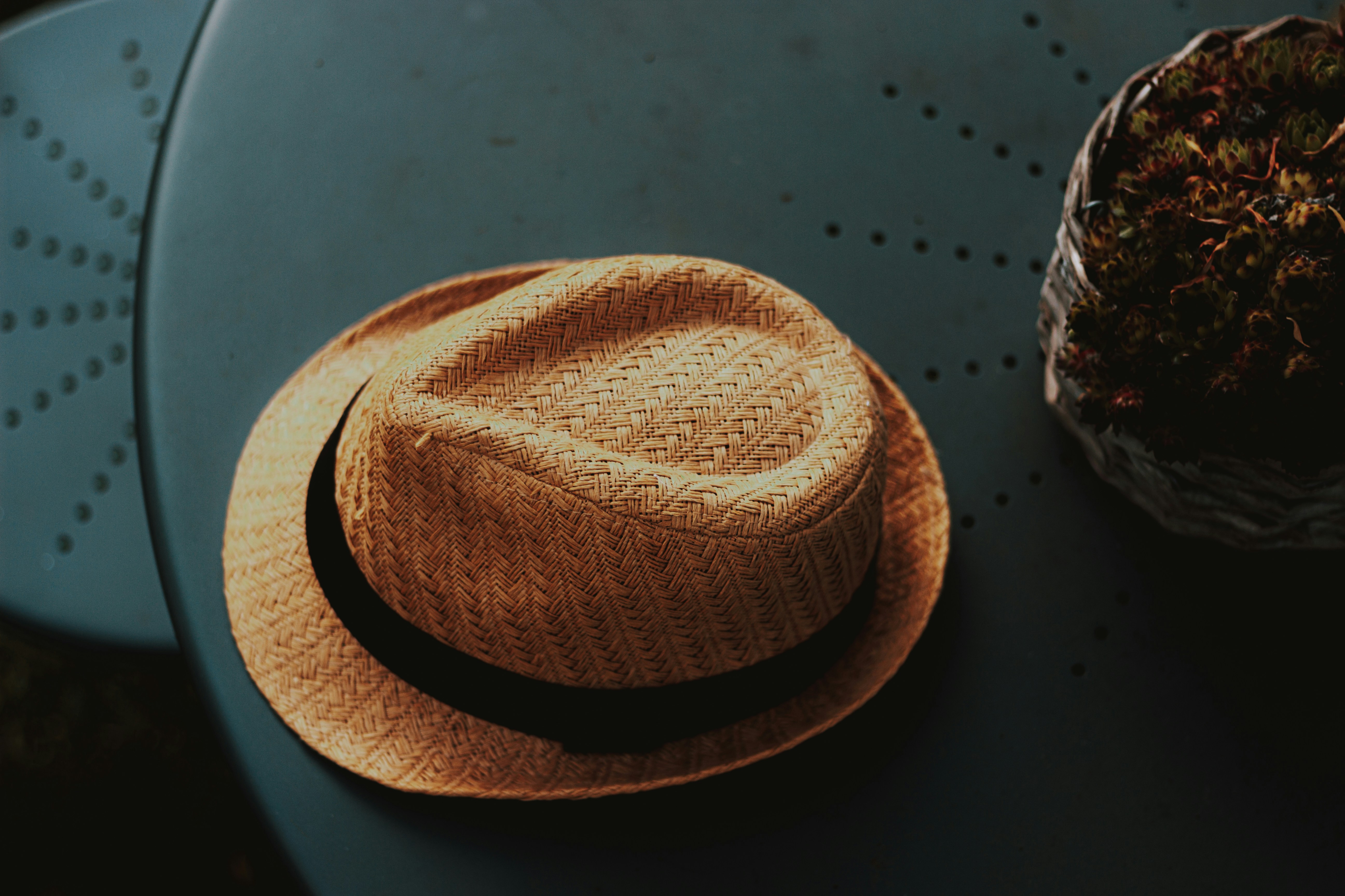 Warm-light straw fedora on a teal metal surface