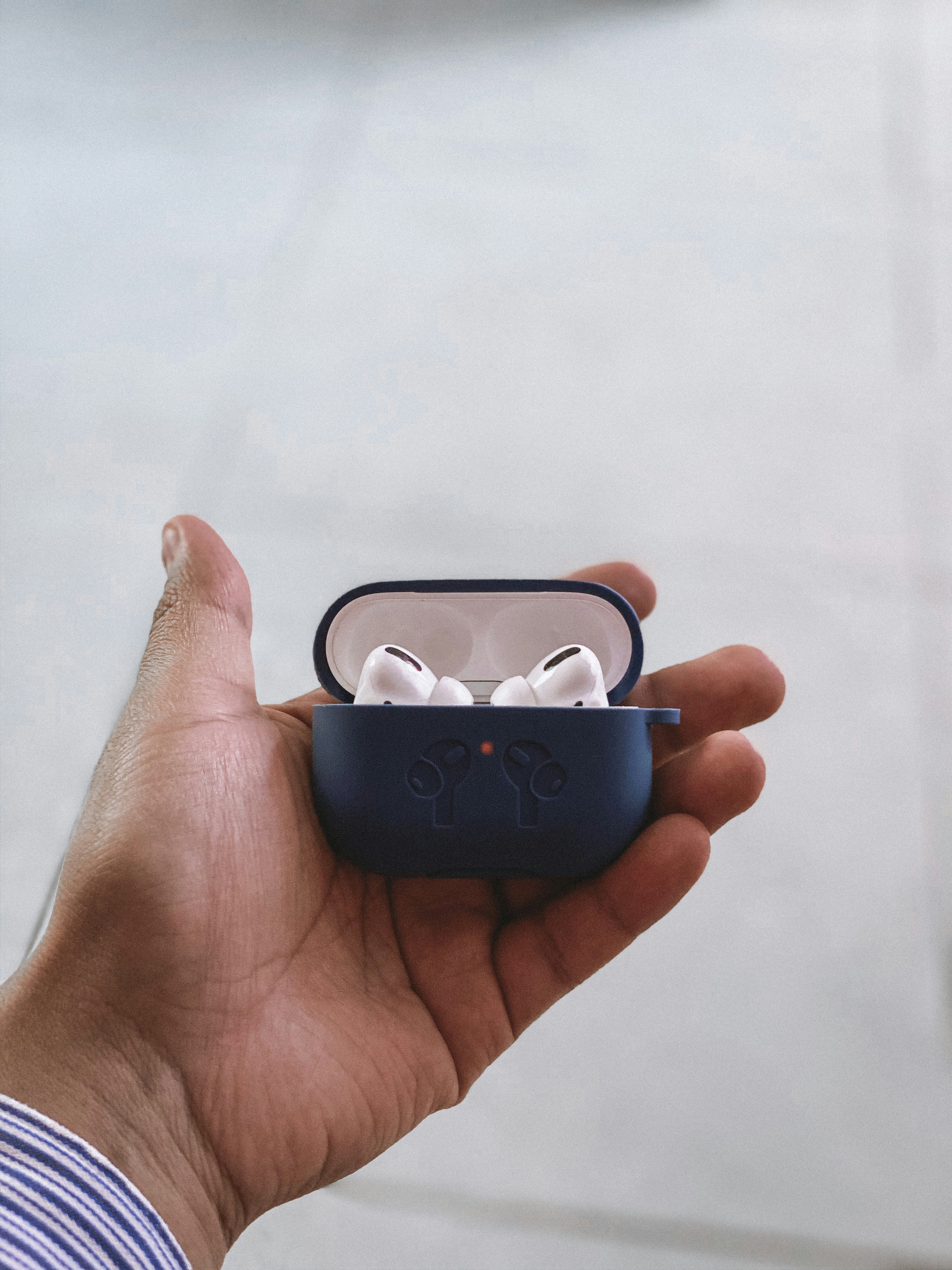 Open AirPods case revealing white earbuds held in a hand against a soft background.
