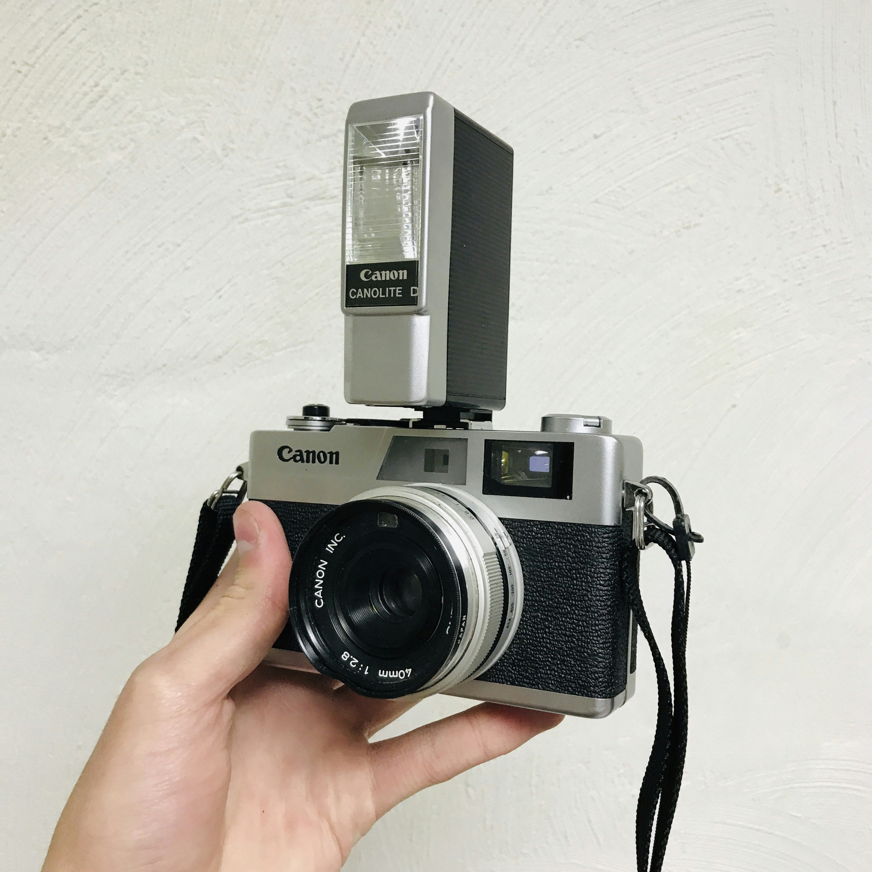 A classic Canon camera held in hand, featuring a flash unit, showcasing retro design elements and craftsmanship.