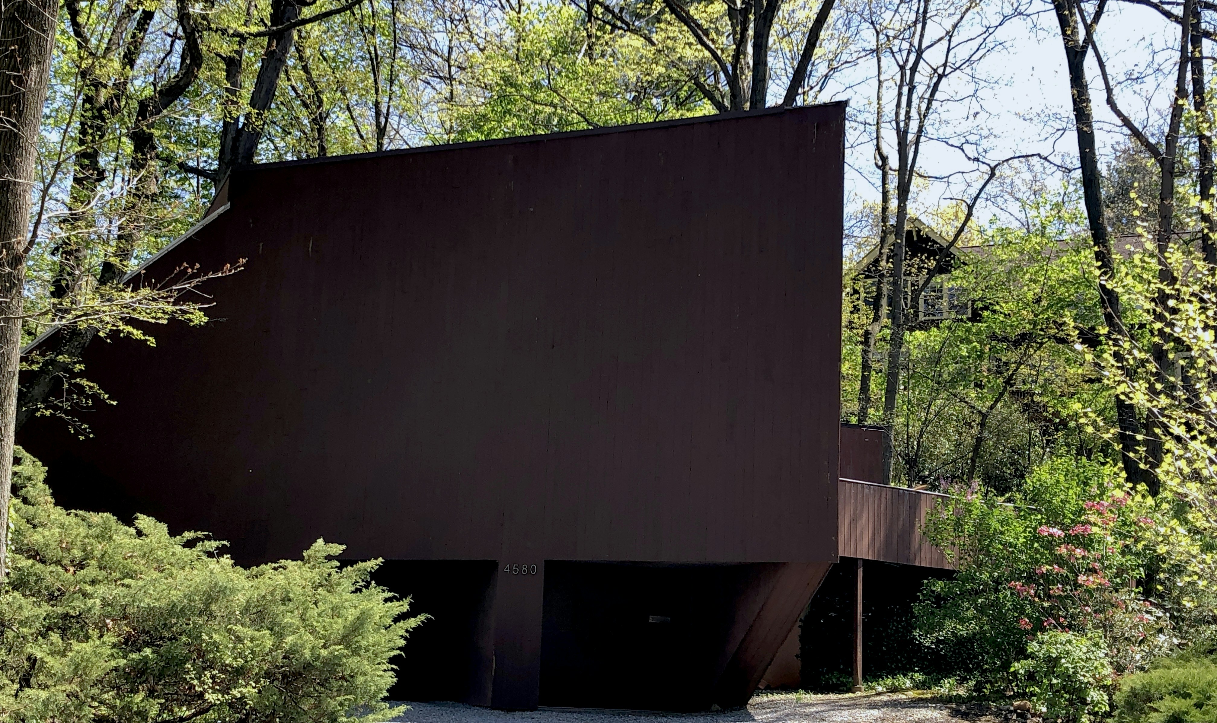 Contemporary dark brown house surrounded by lush green trees under a clear sky.