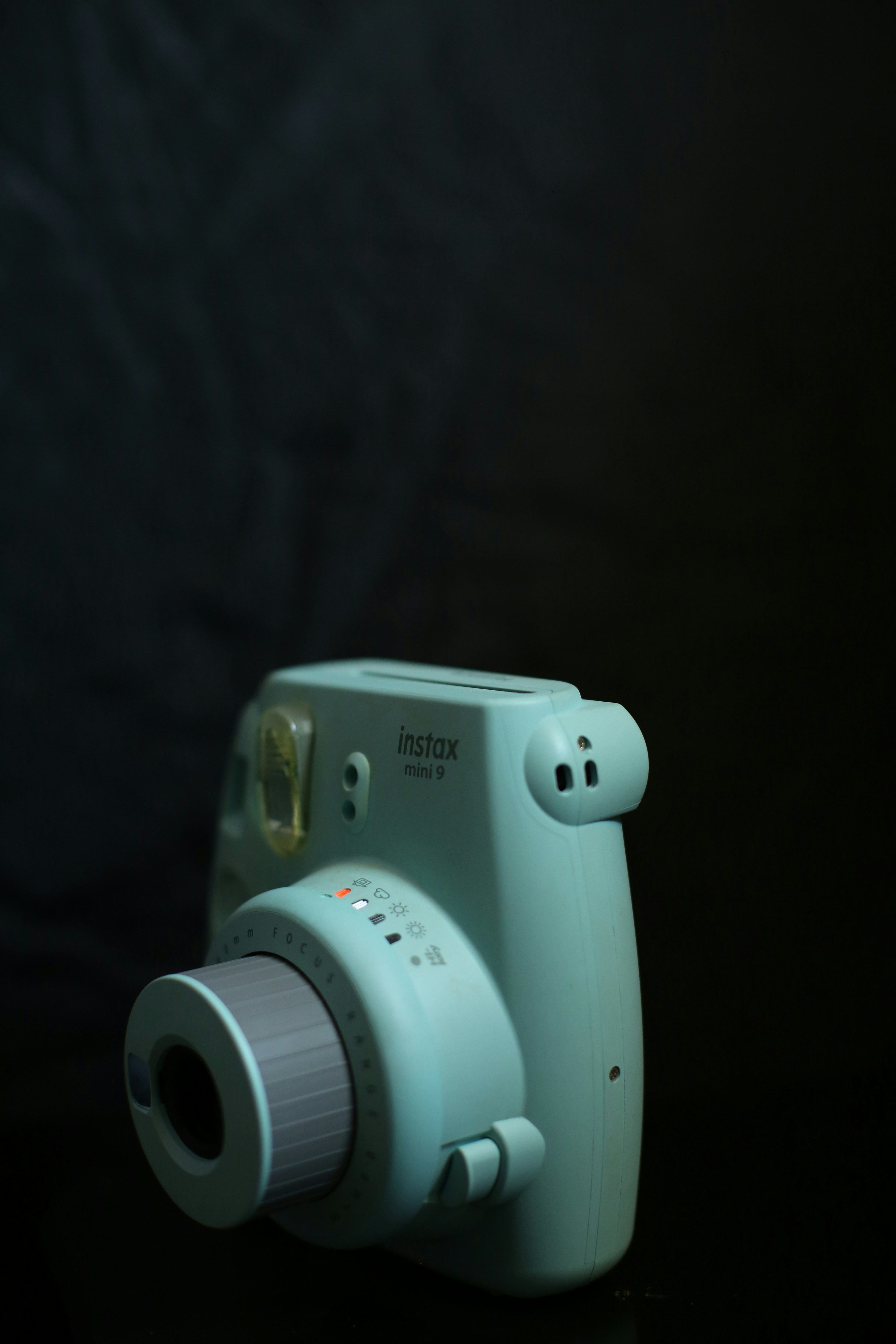Light blue instant camera with a sleek design, showcasing its lens and controls against a dark background.