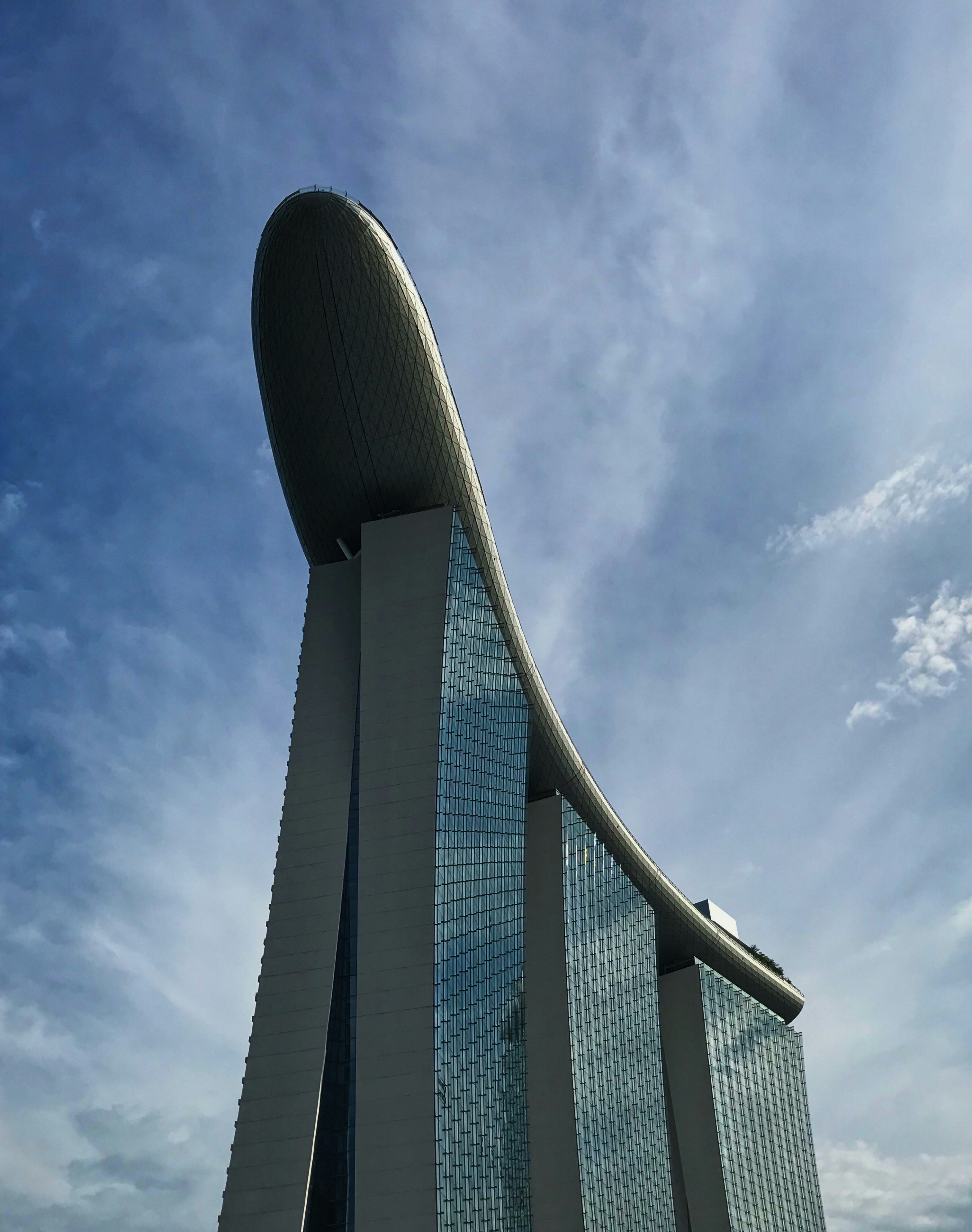 Sleek skyscraper with a distinctive curved rooftop against a backdrop of dynamic clouds.