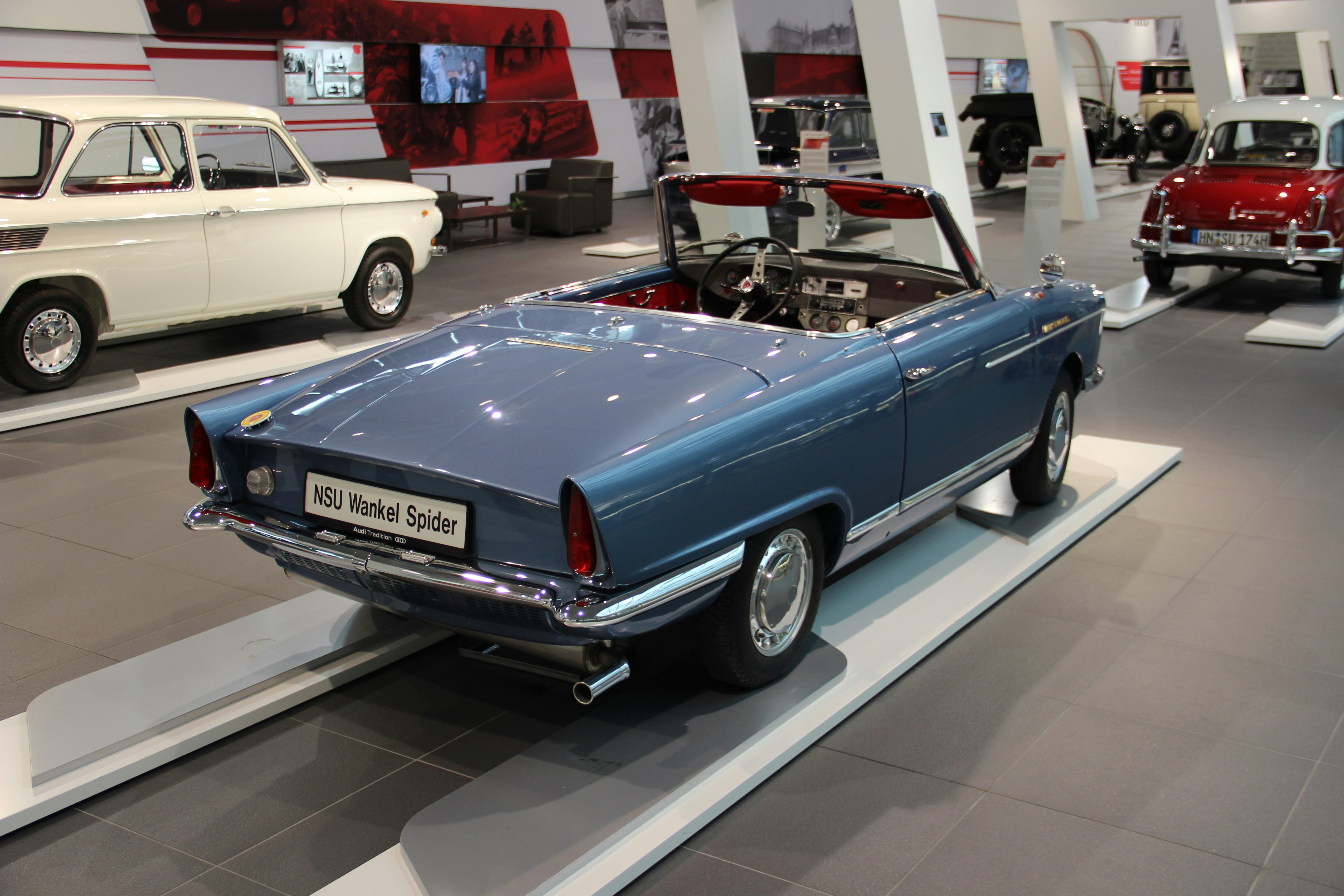 Vintage blue convertible displayed in a modern showroom alongside other classic cars.