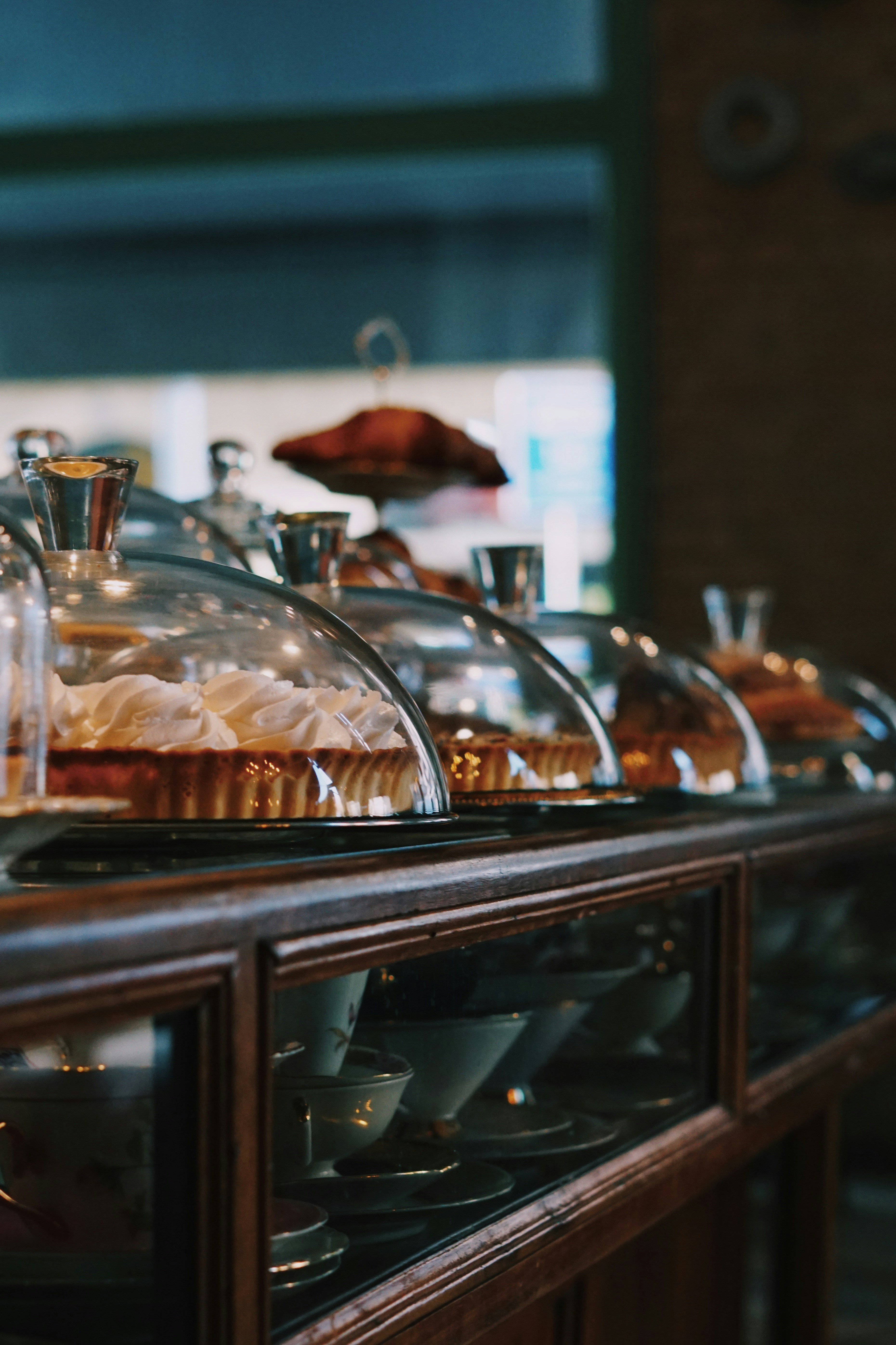 A display of elegantly covered pastries under glass domes in a cozy café setting, highlighting the allure of desserts. The warm tones and soft lighting create an inviting atmosphere.