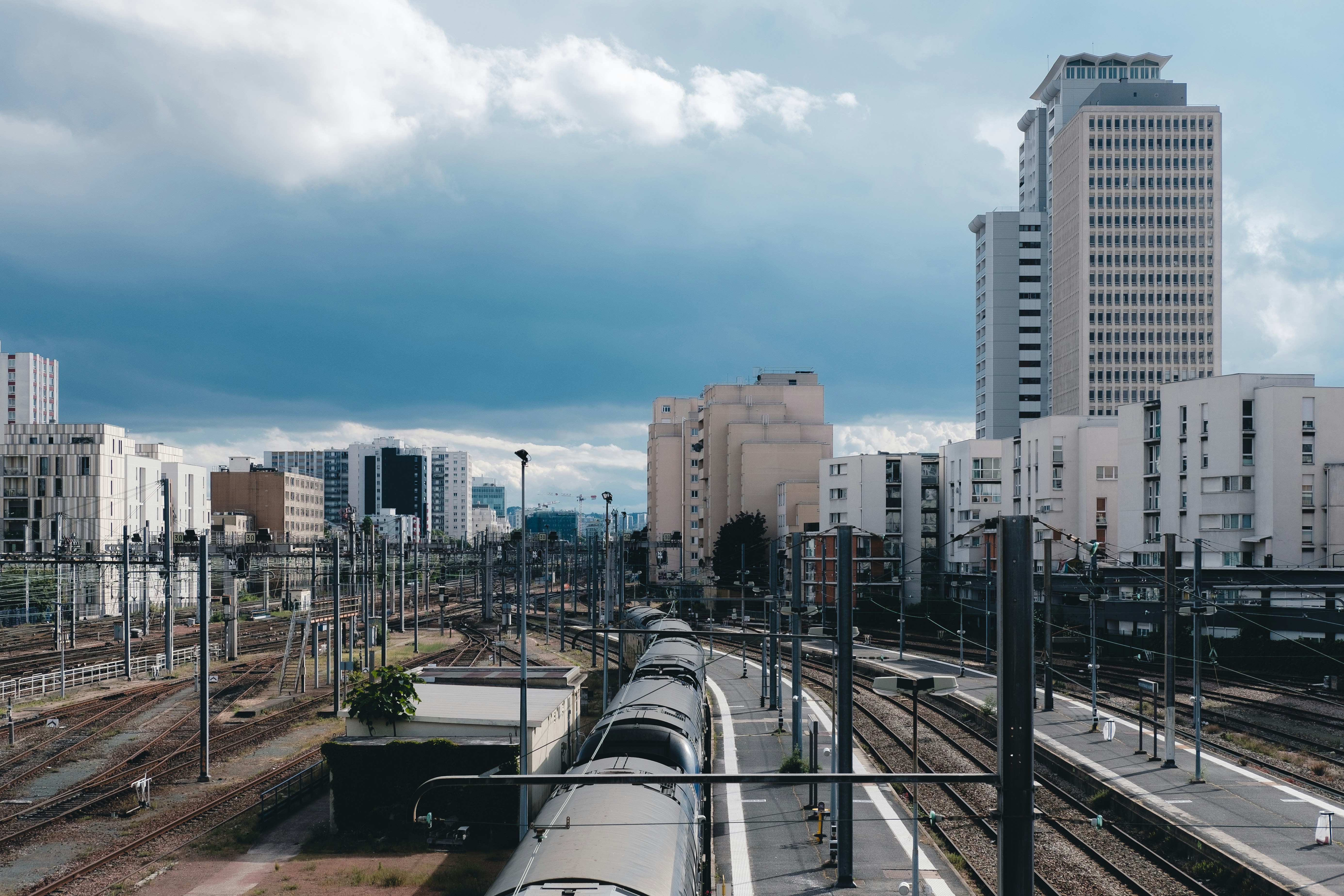 A railway network weaving through an urban landscape, framed by modern skyscrapers under a cloudy sky.