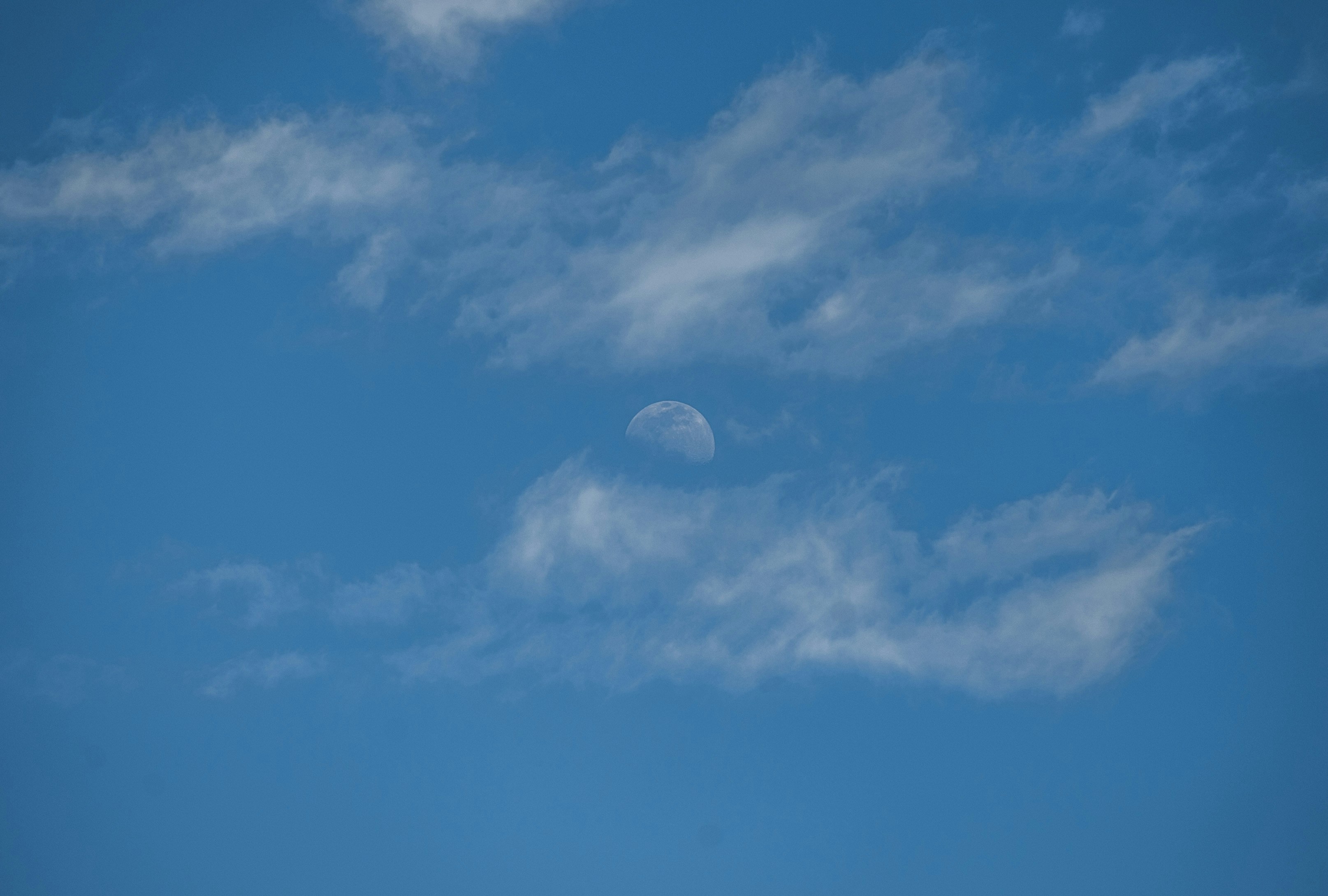 Moon partially obscured by wispy clouds in a clear blue sky.