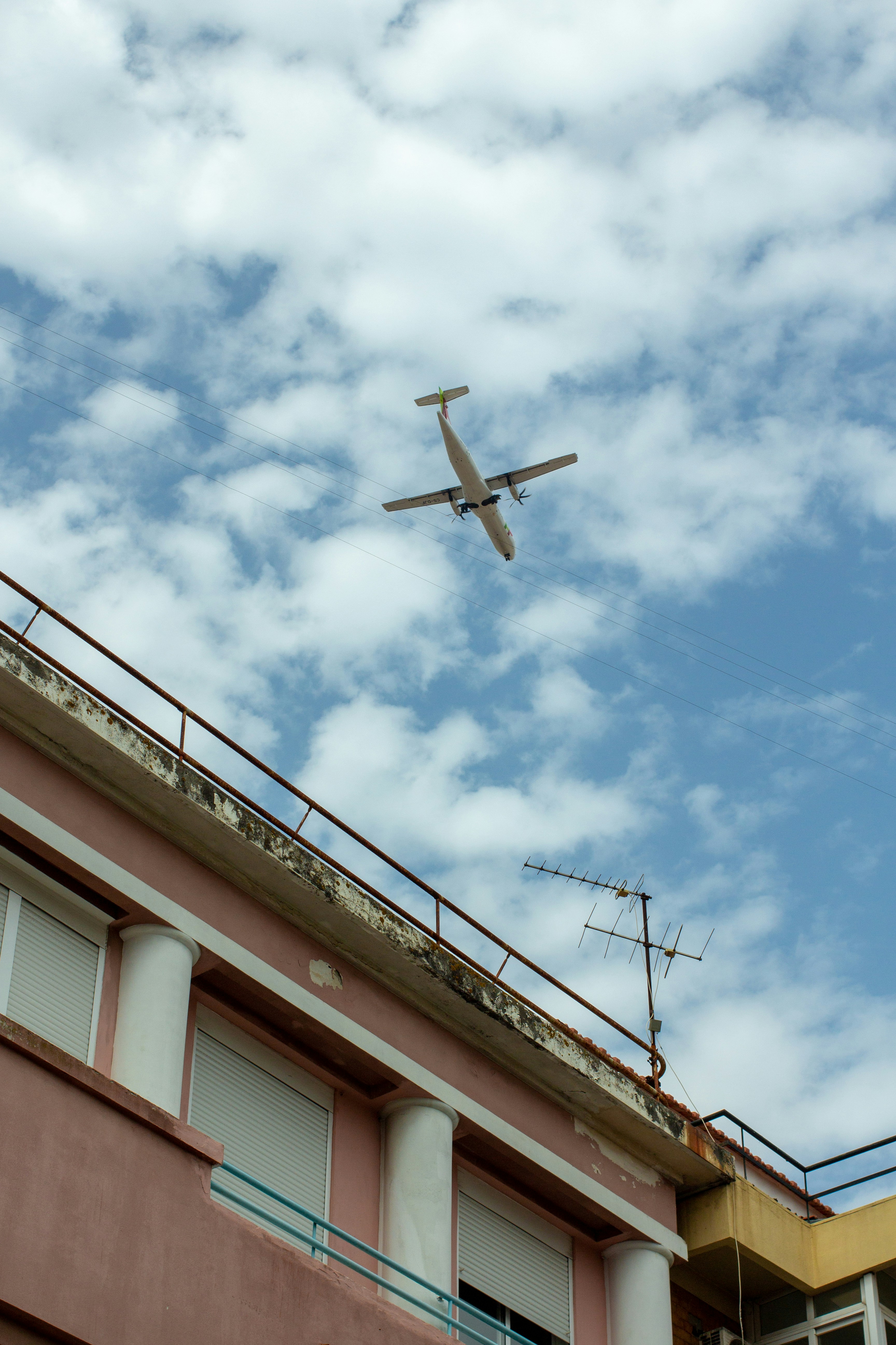 Rooftop Horizon: A Tiny Plane Traverses a Cloudy Blue Sky