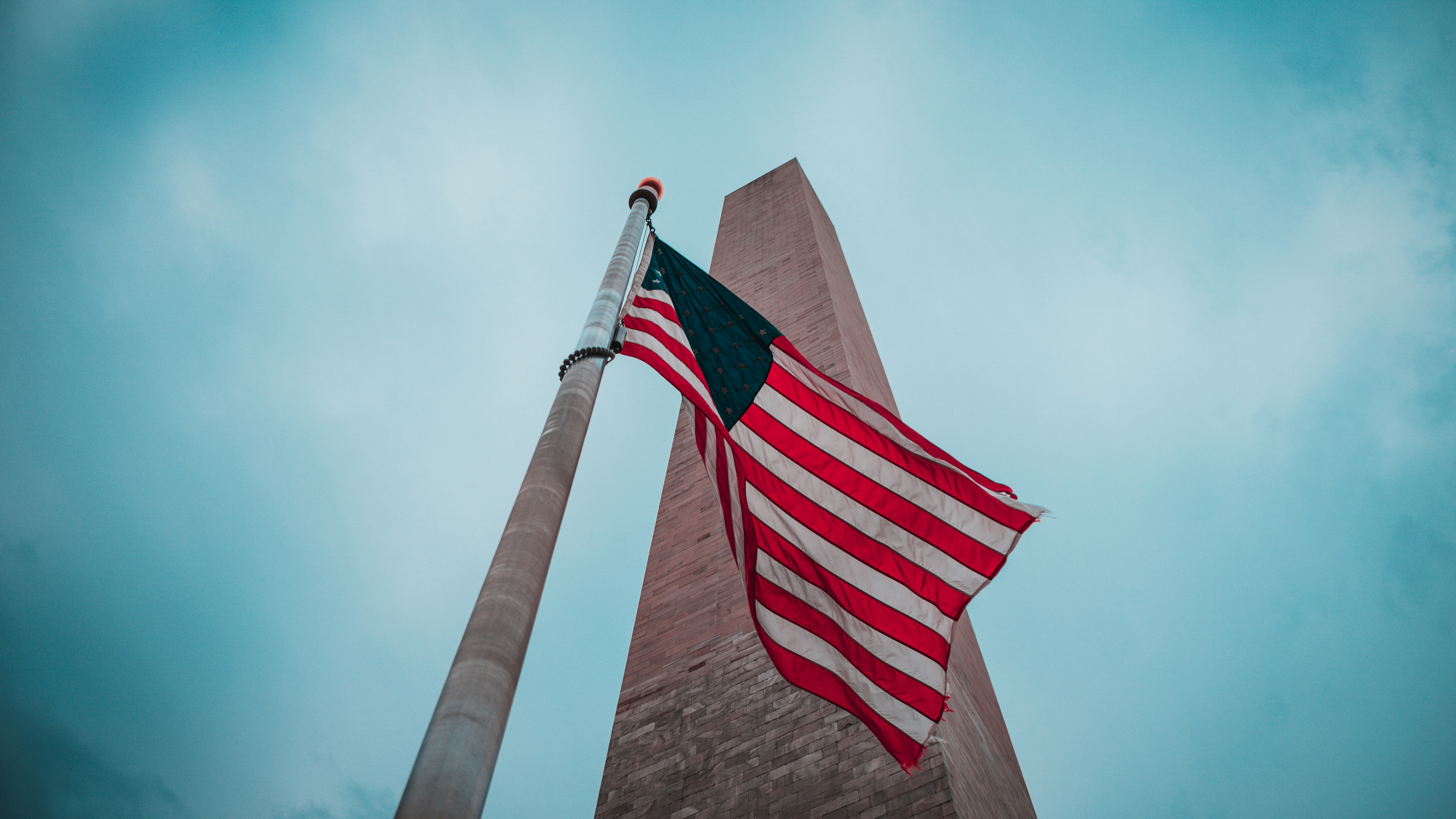 American flag billowing beside a towering obelisk against a moody sky.