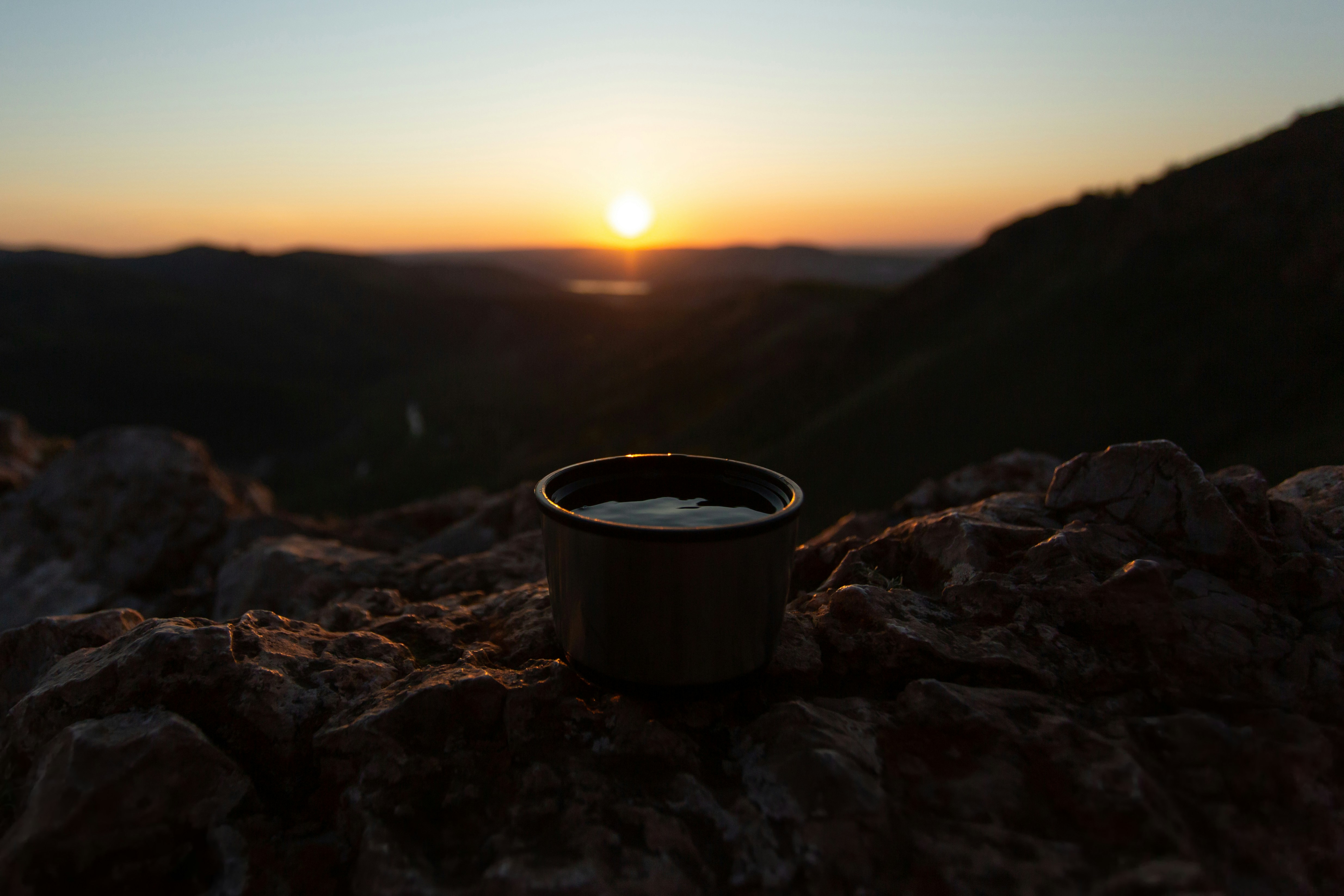 Dawn sip: cup perched on rugged ridge as sun spills over distant valleys