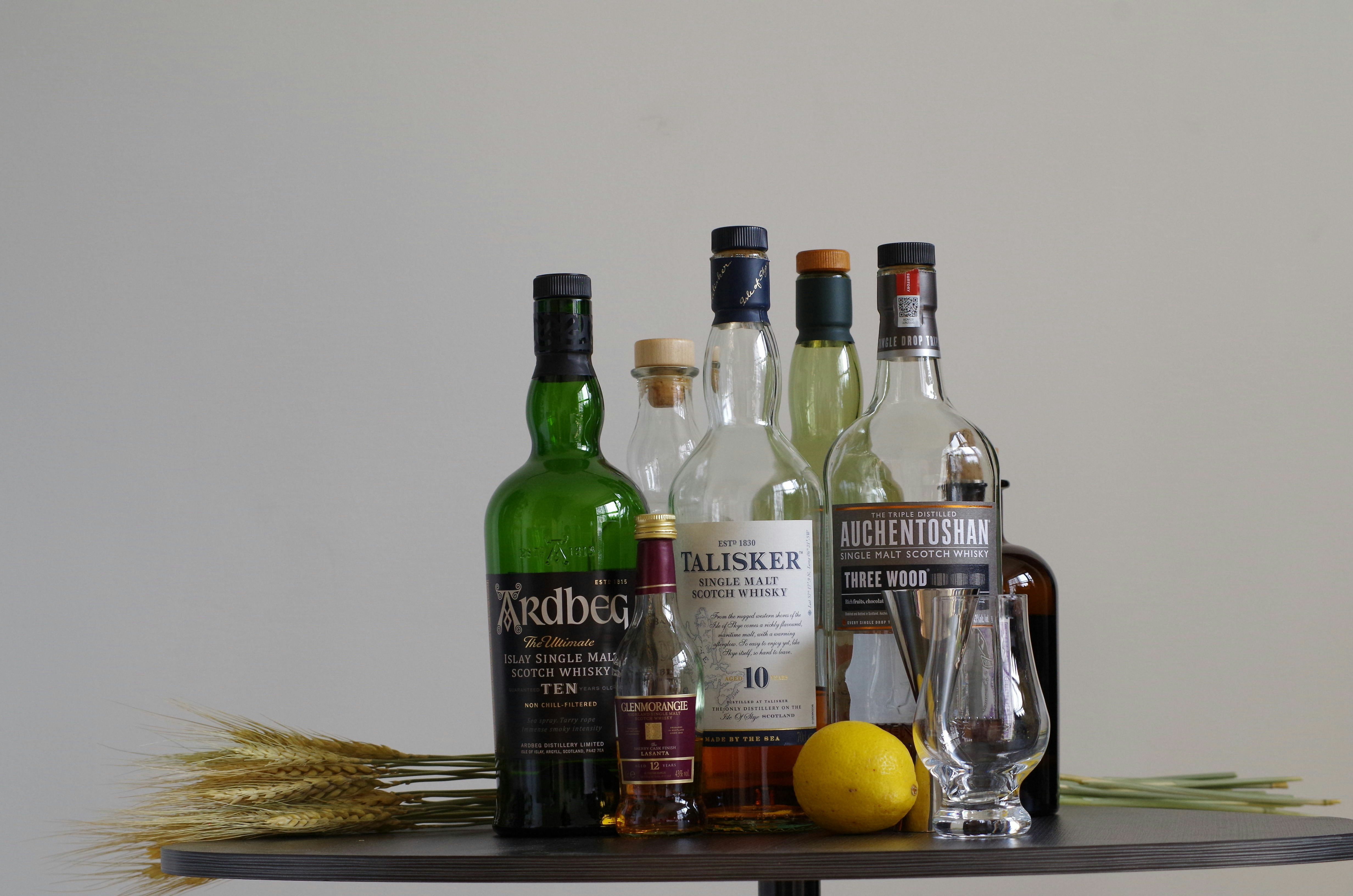 A still-life arrangement of liquor bottles and a lemon on a dark table, with a blurred neutral background.