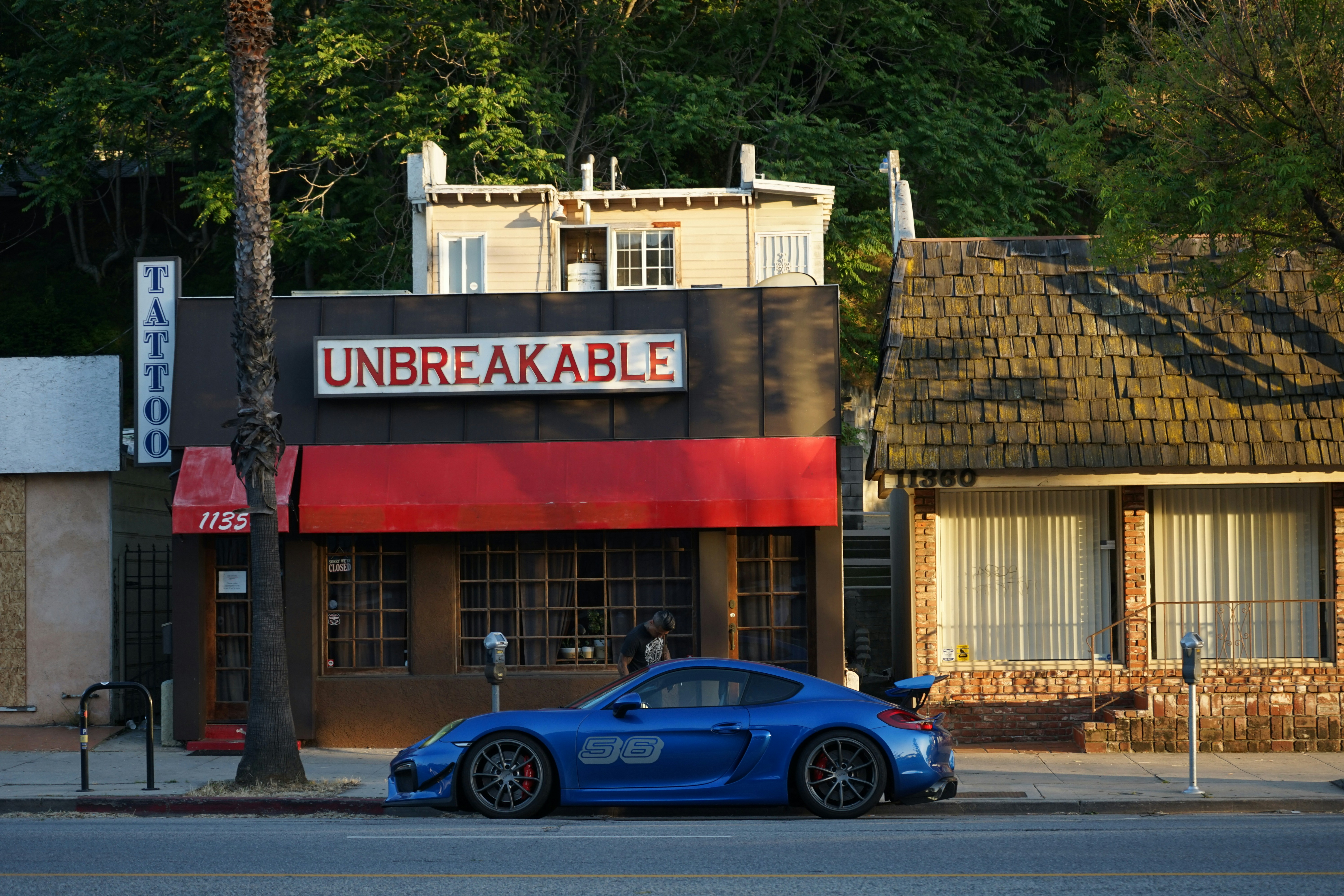 A striking blue sports car parked in front of a bold 'UNBREAKABLE' storefront, showcasing a blend of urban culture and automotive design.