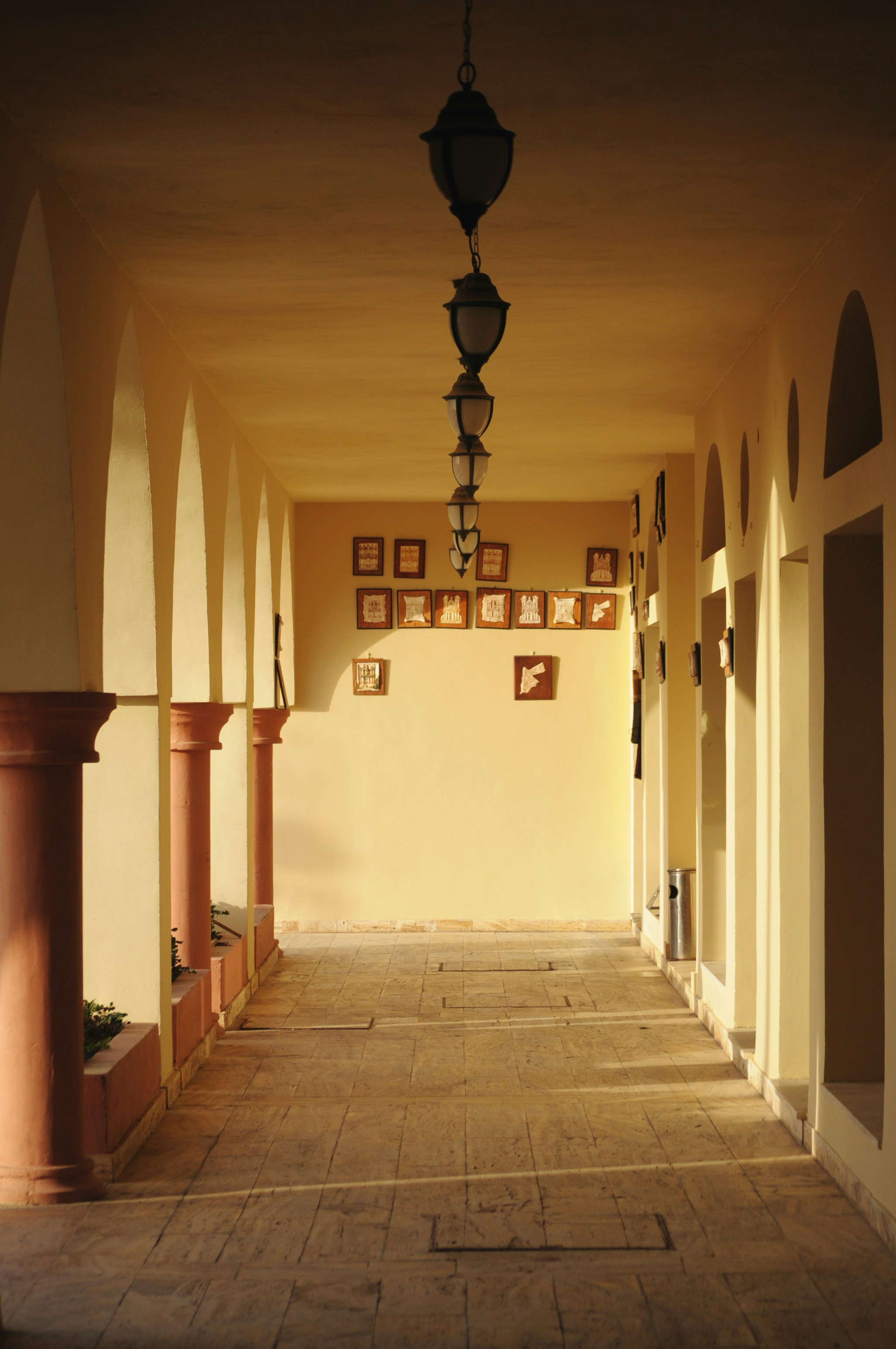 Sunlit corridor featuring arches and decorative frames along the walls, creating a serene atmosphere. The warm tones enhance the inviting feel of the space.