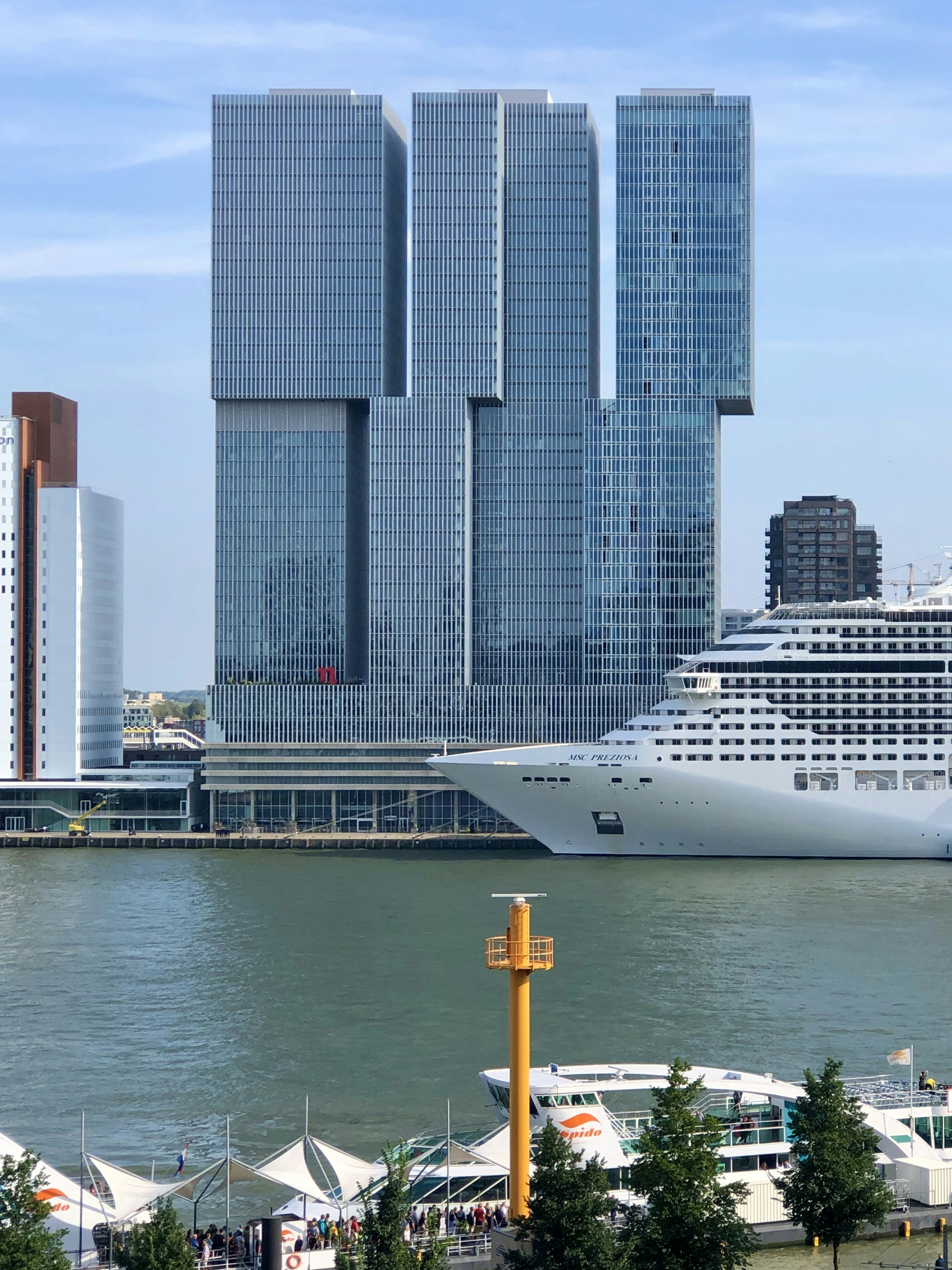 Modern skyscrapers reflect in the water, alongside a large cruise ship docked at the harbor. The scene captures the interplay of architecture and maritime activity.