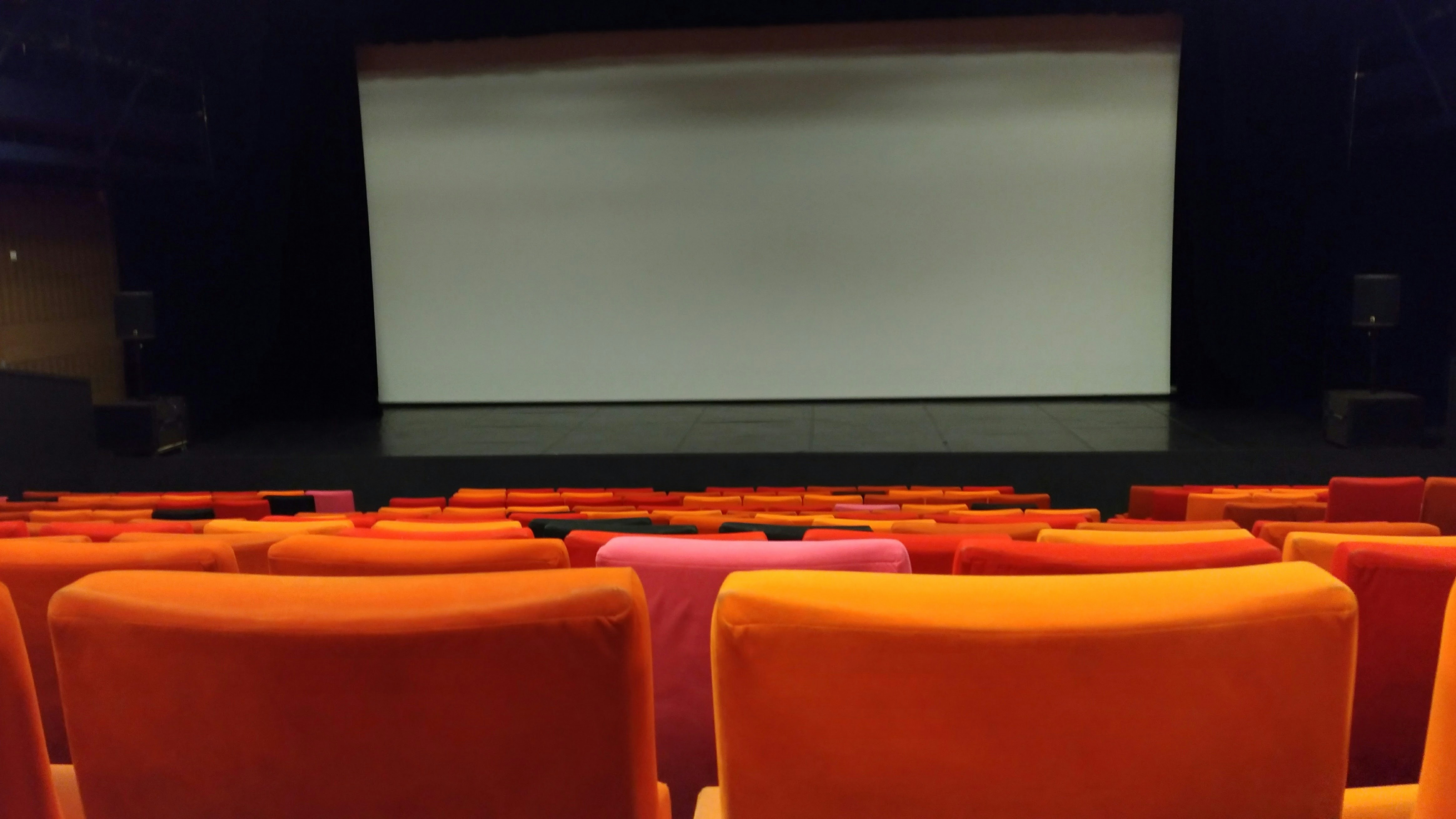 Colorful seating arrangement in a theater with a large blank screen, setting the stage for an upcoming film. 