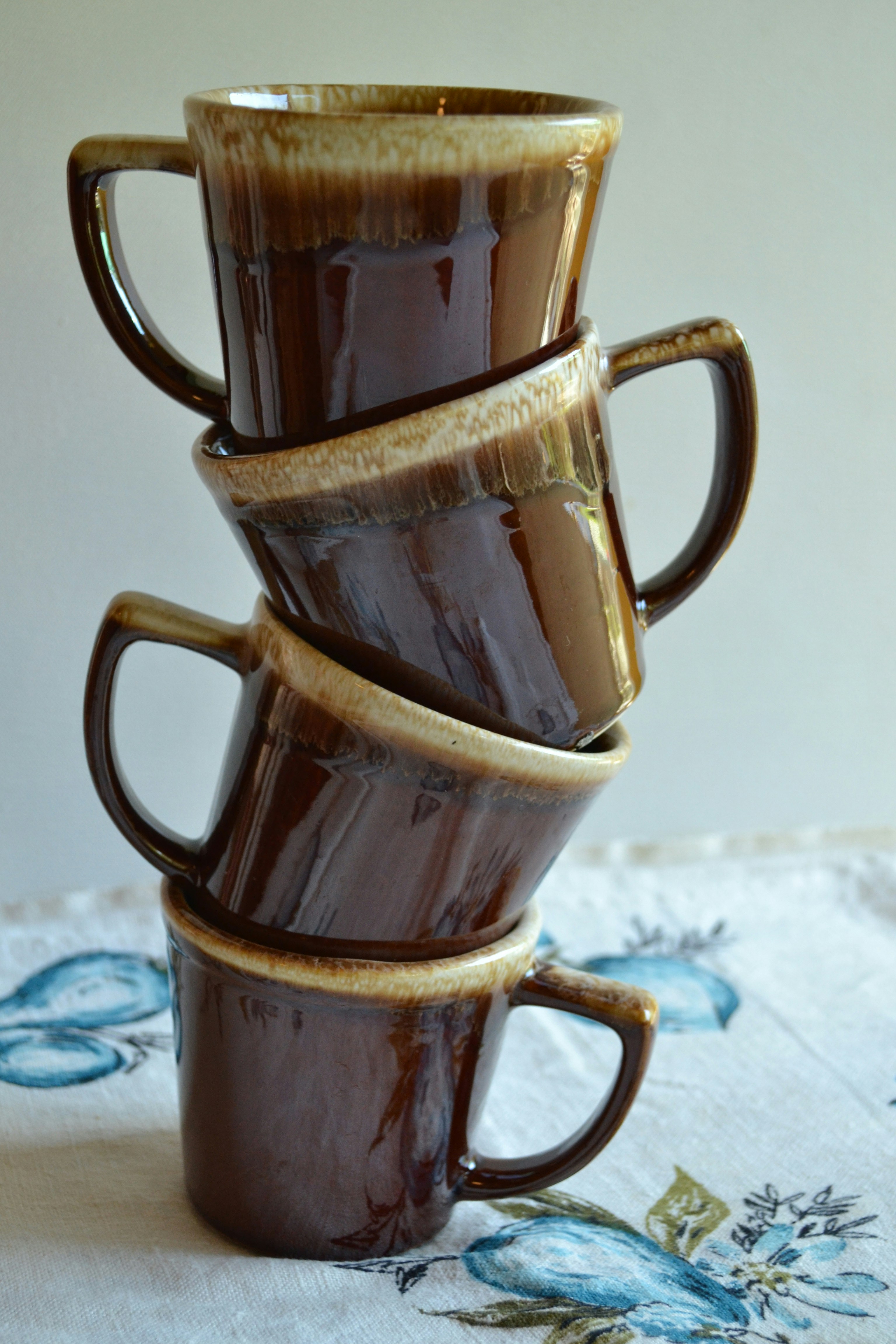 Leaning Tower of Brown: Four Ceramic Mugs Stacked on a Floral Tablecloth
