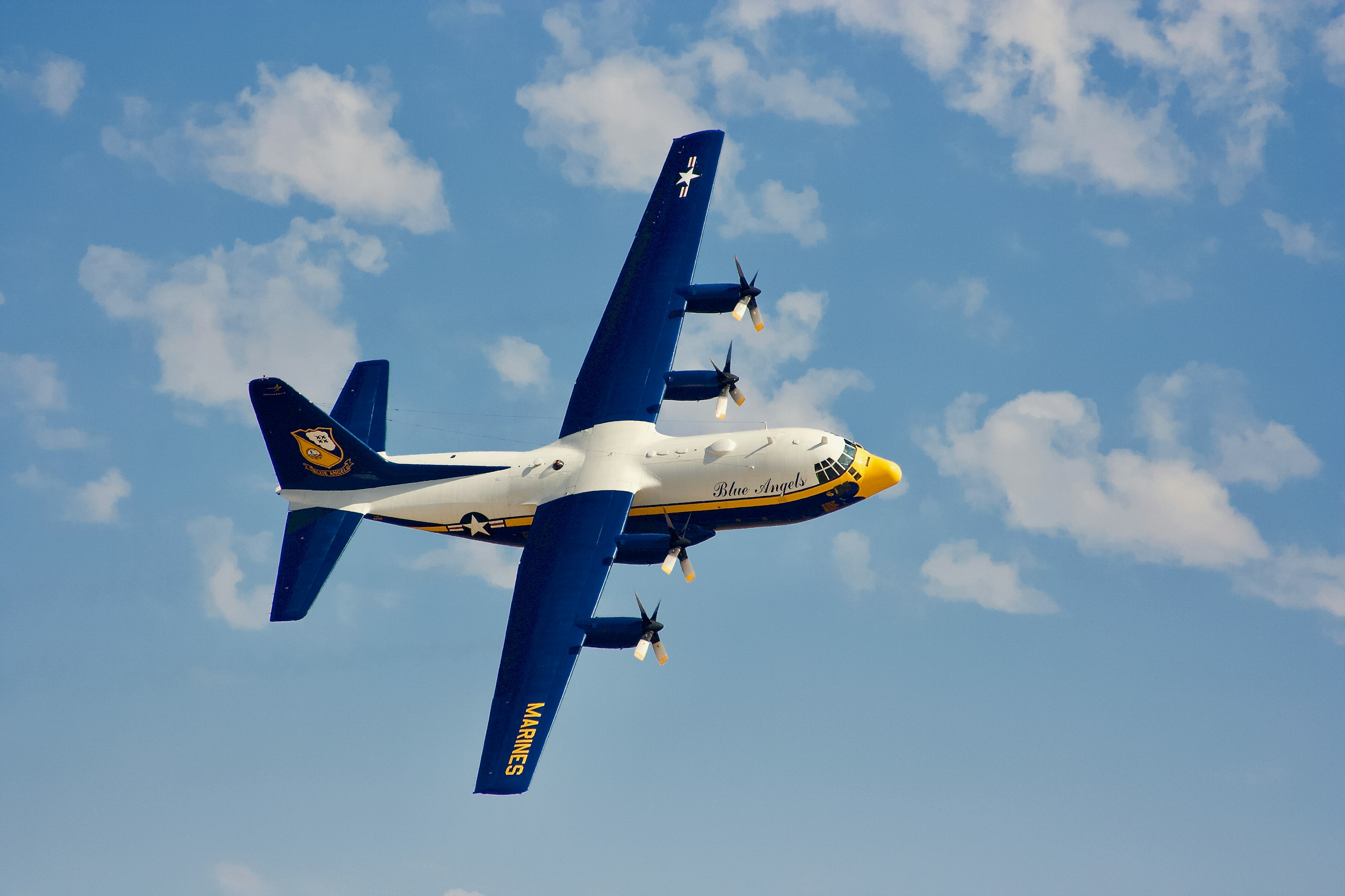 Blue Angels C-130 Hercules performing a maneuver against a backdrop of scattered clouds.