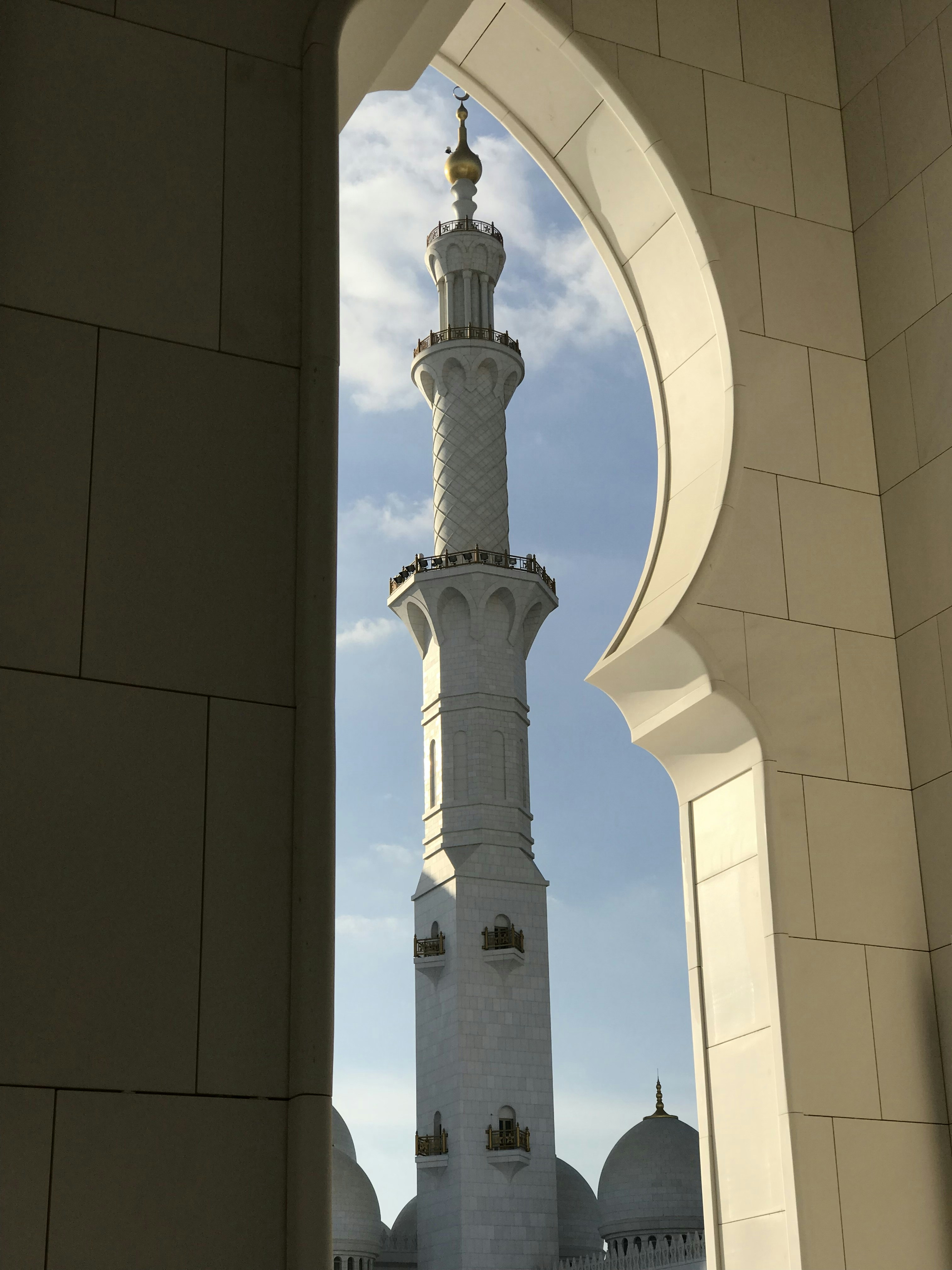 Minaret of a grand mosque framed by intricate architectural arches under a clear blue sky.
