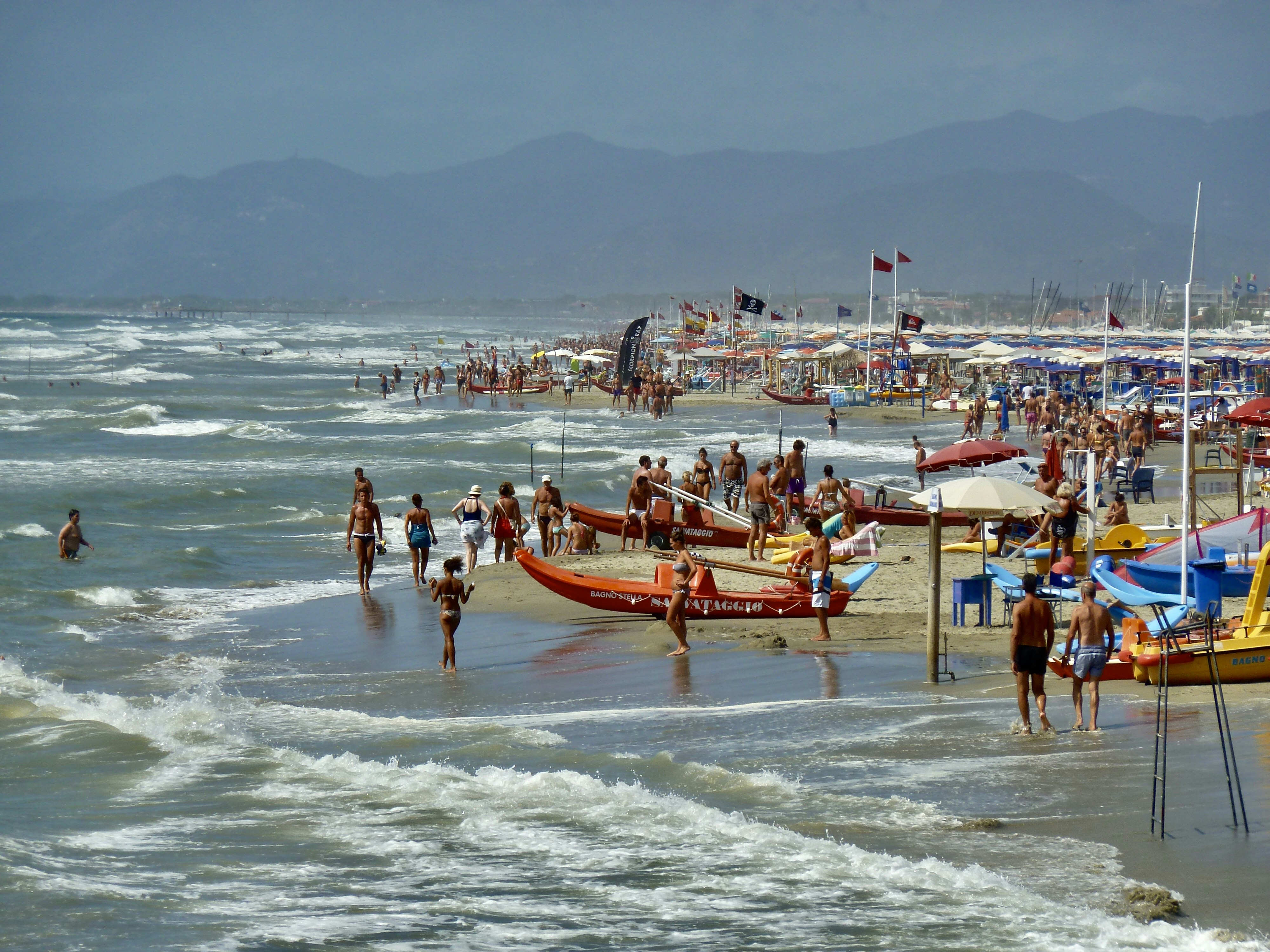 Crowded beach scene with people enjoying the waves and sunbathing on a sunny day.