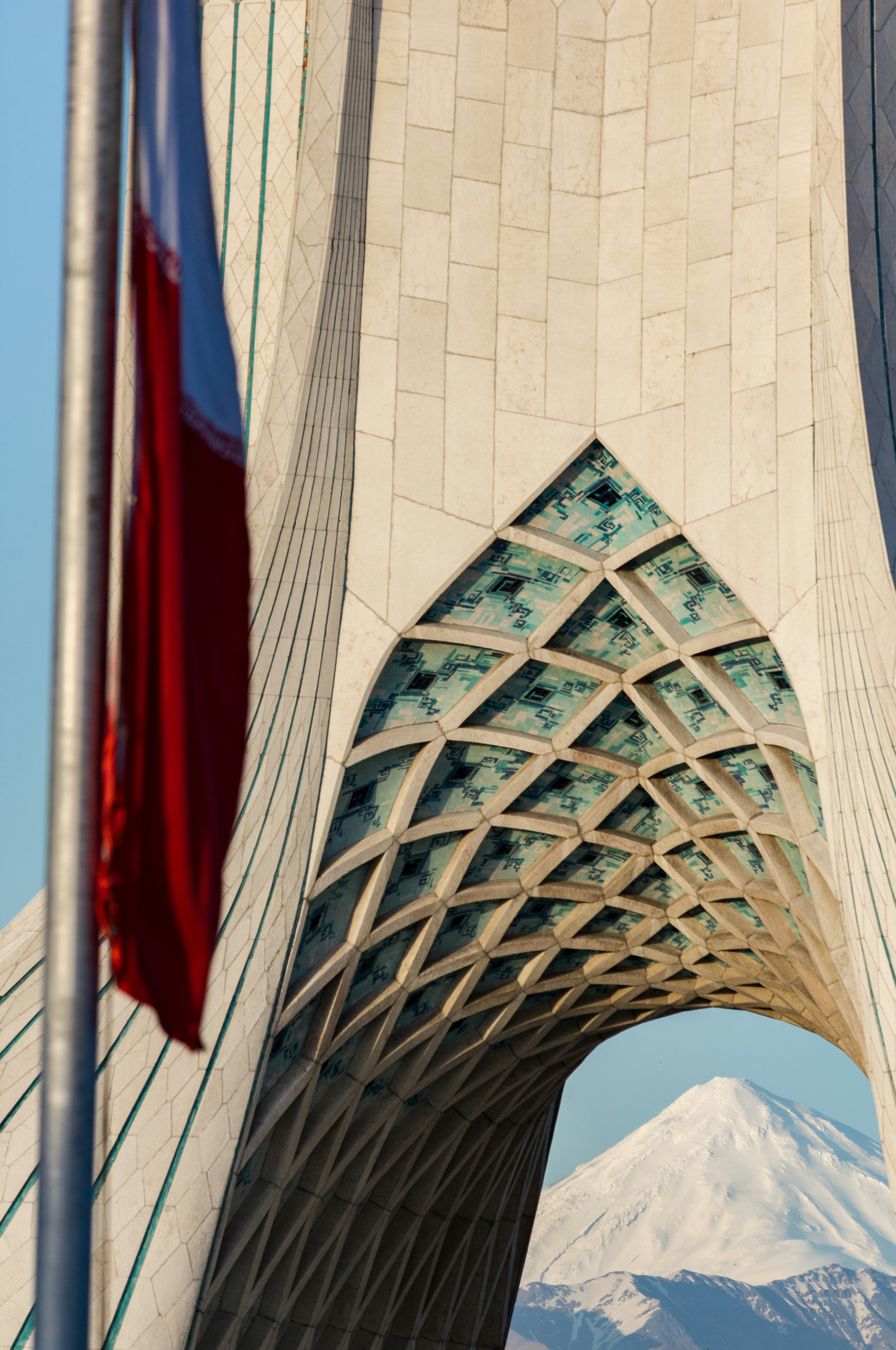 Intricate geometric design of a monument with a snow-capped mountain in the background, framed by a red and white flag.