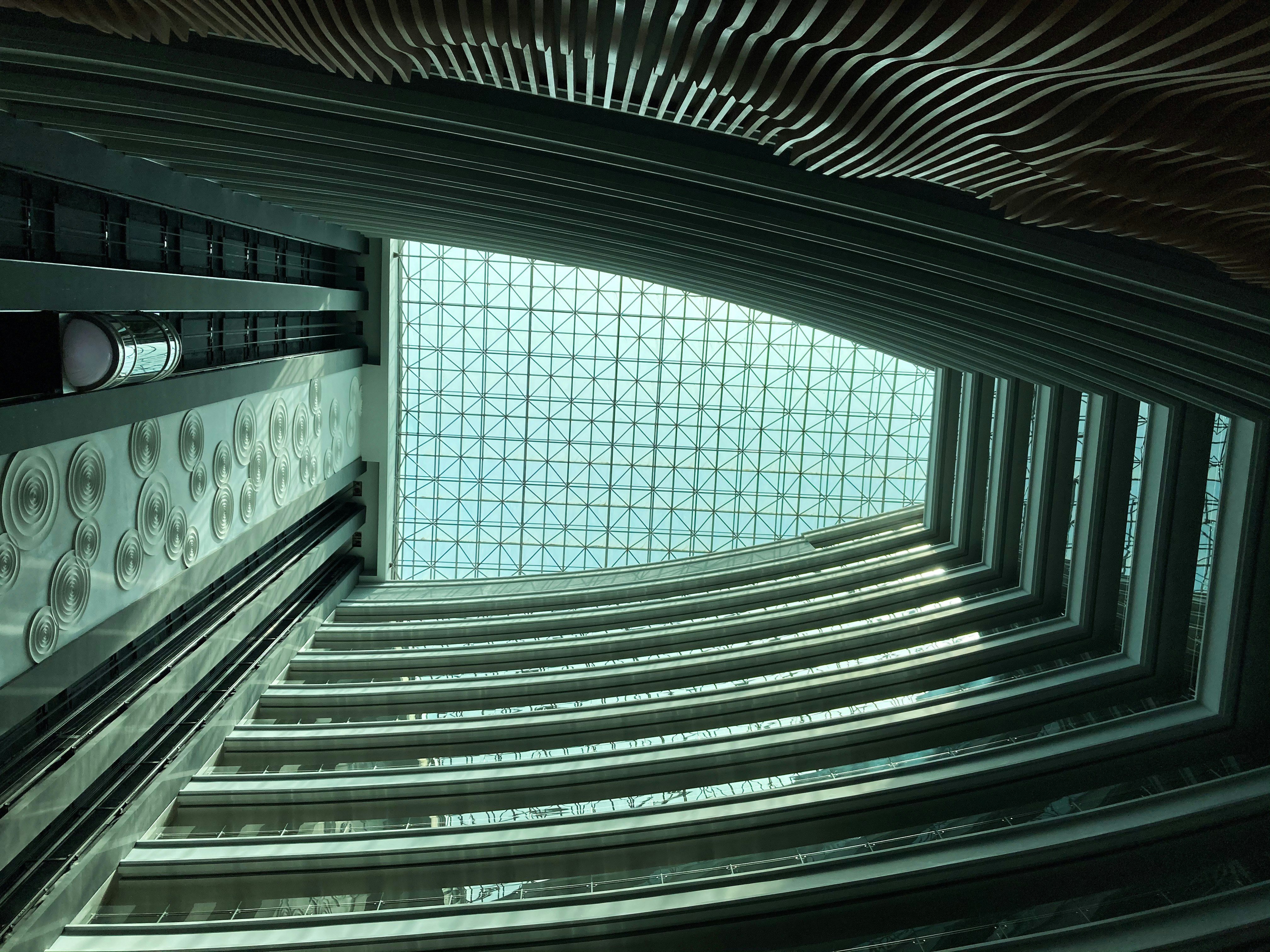 Looking up at a multi-story atrium with layered balconies and a skylight, creating a symmetrical pattern.