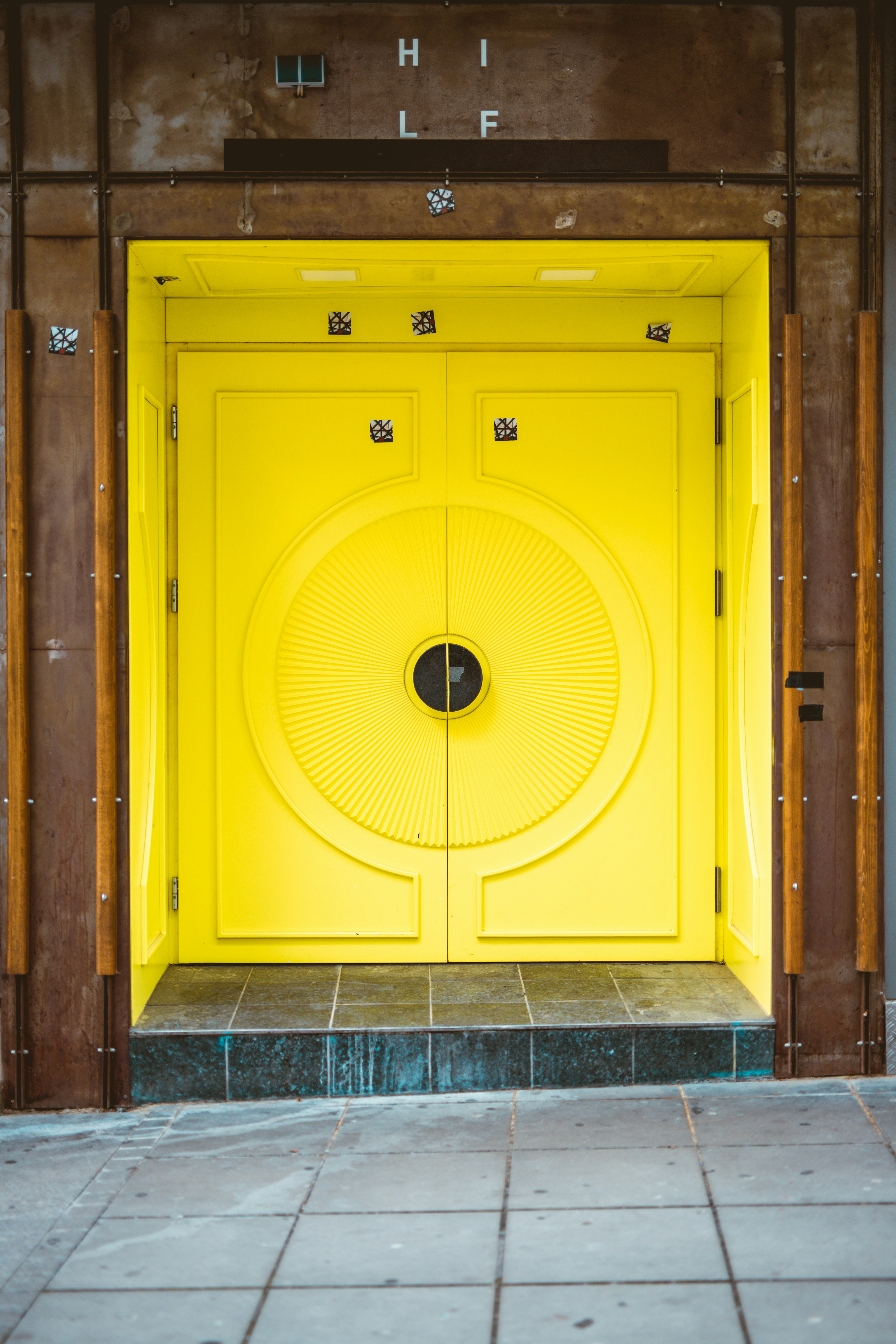 Bright yellow double doors with a circular design and wooden accents create an inviting entrance. The unique pattern draws attention to the center point.