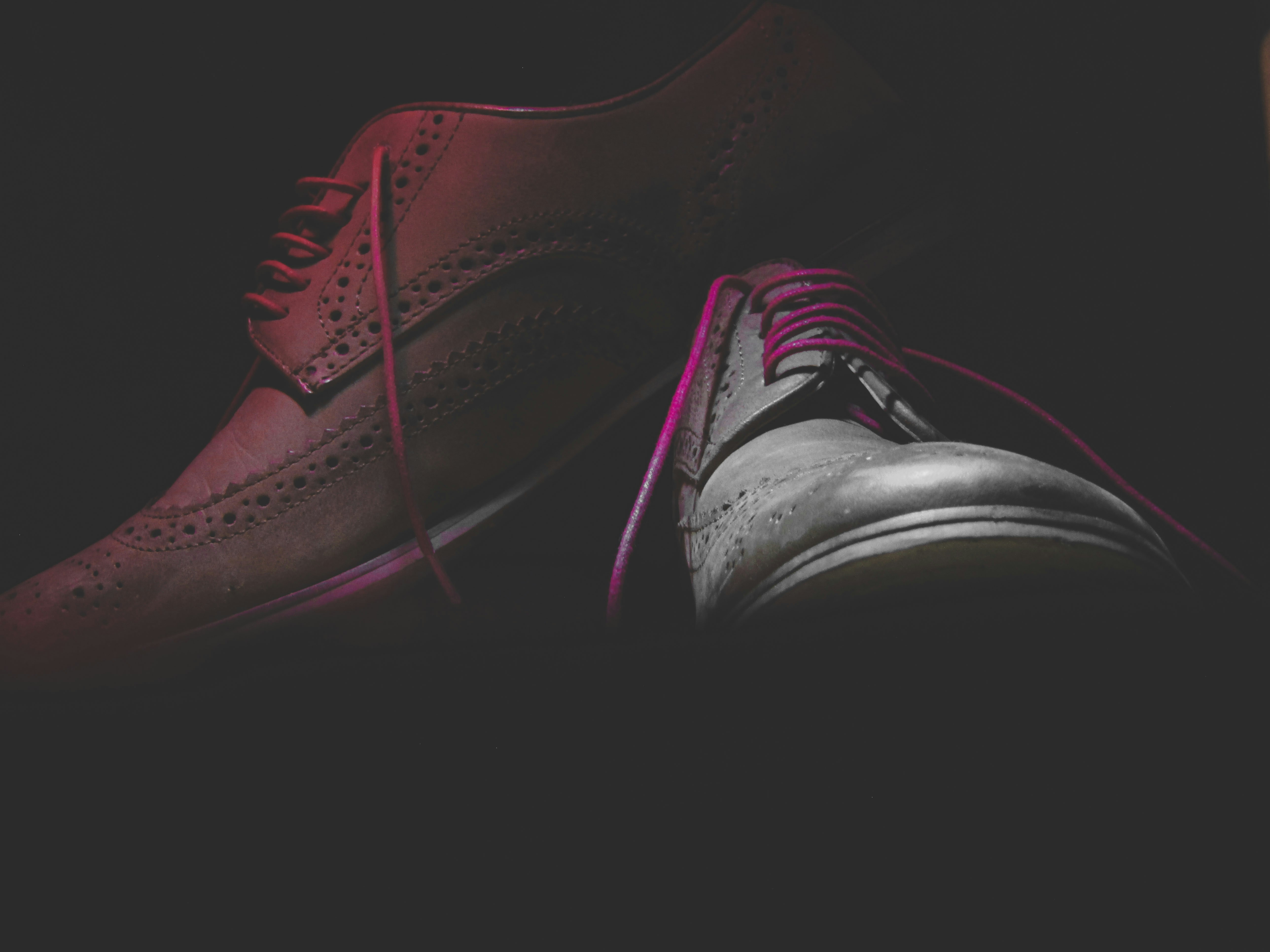 Two pairs of shoes, one light and one dark, elegantly displayed with contrasting laces. The dramatic lighting highlights their textures and details.