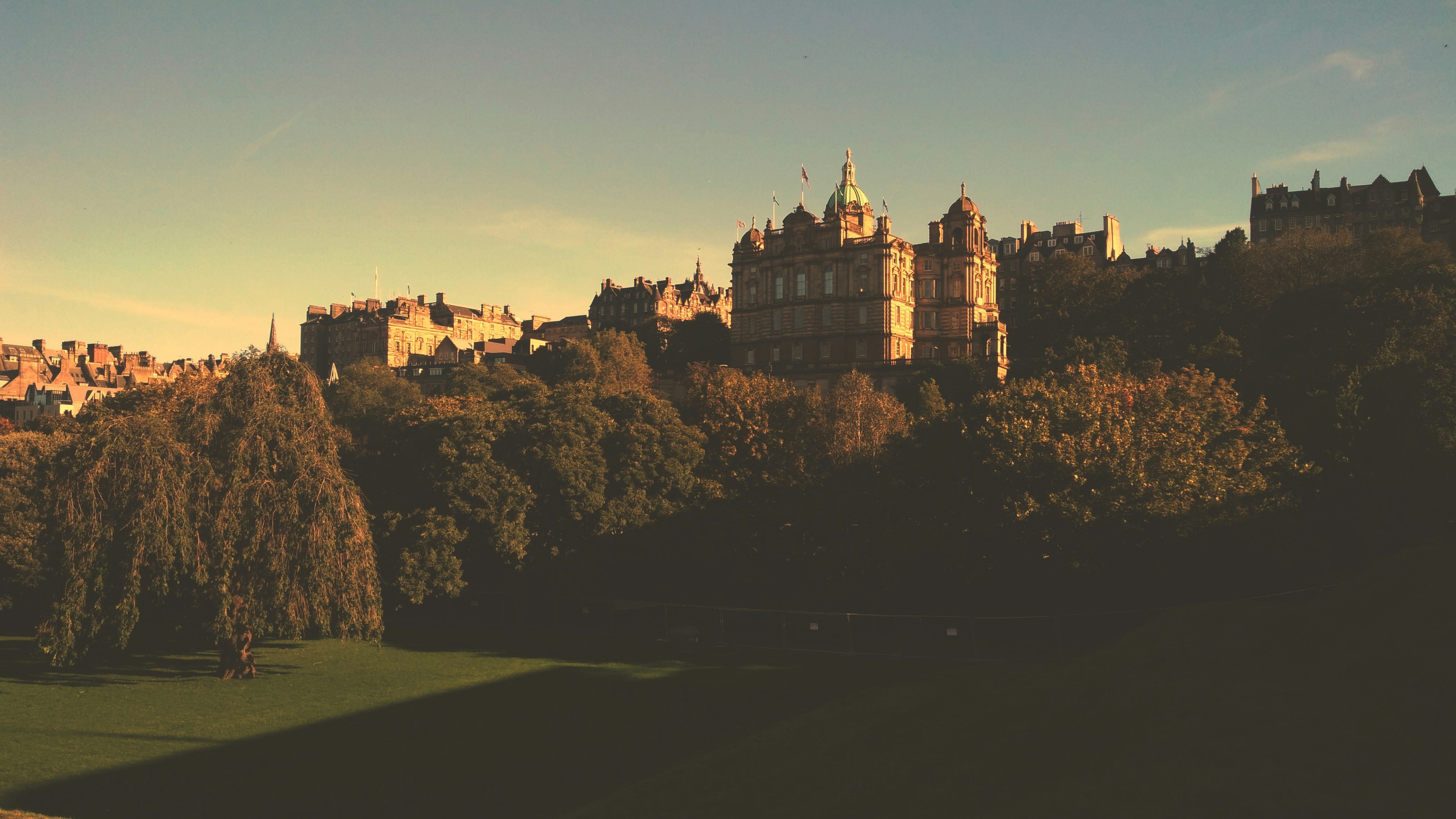 Sunlit Edinburgh skyline with historic buildings and lush greenery under a clear sky.