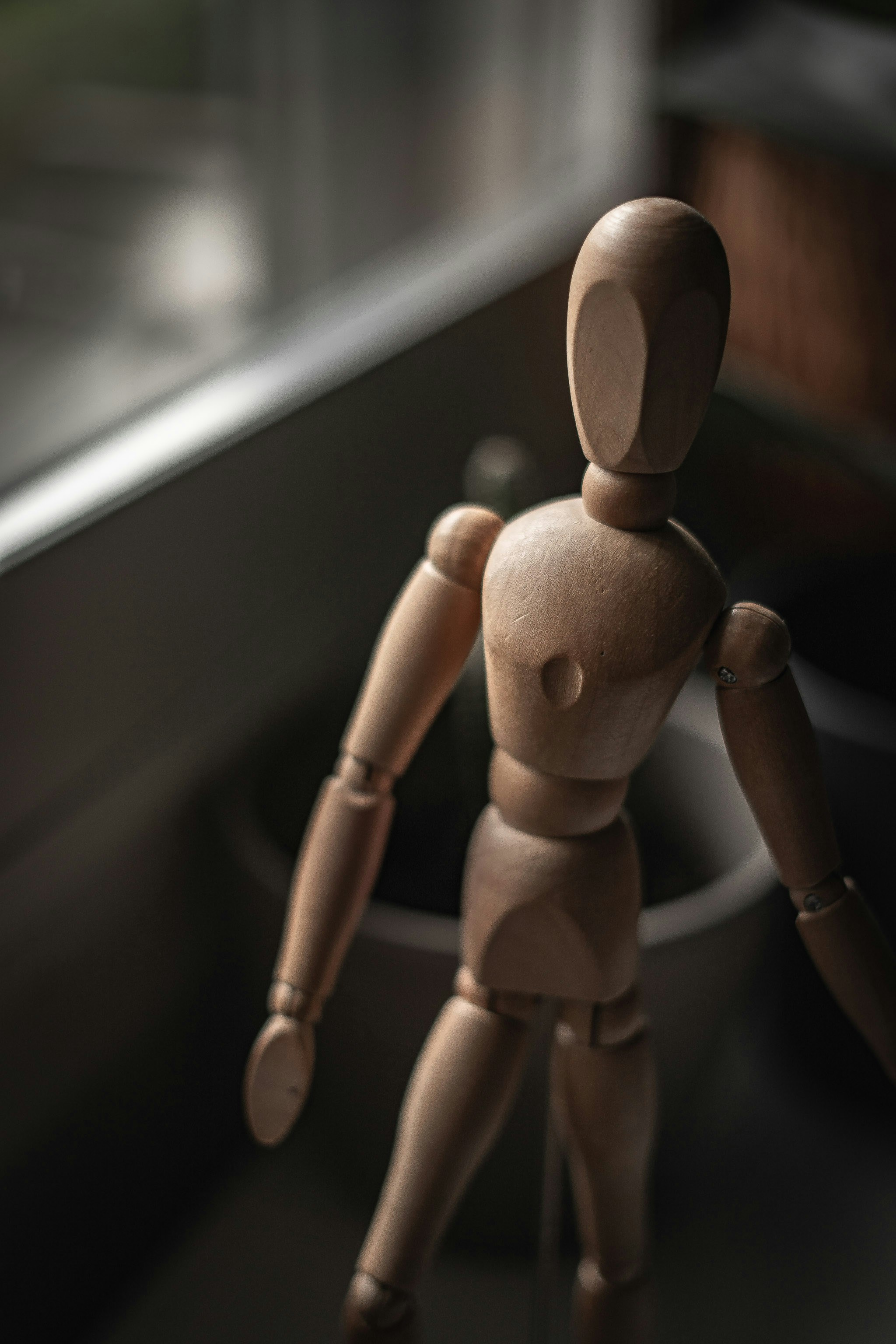A wooden mannequin posed in a softly lit interior, highlighting its natural grain and form against a blurred background.