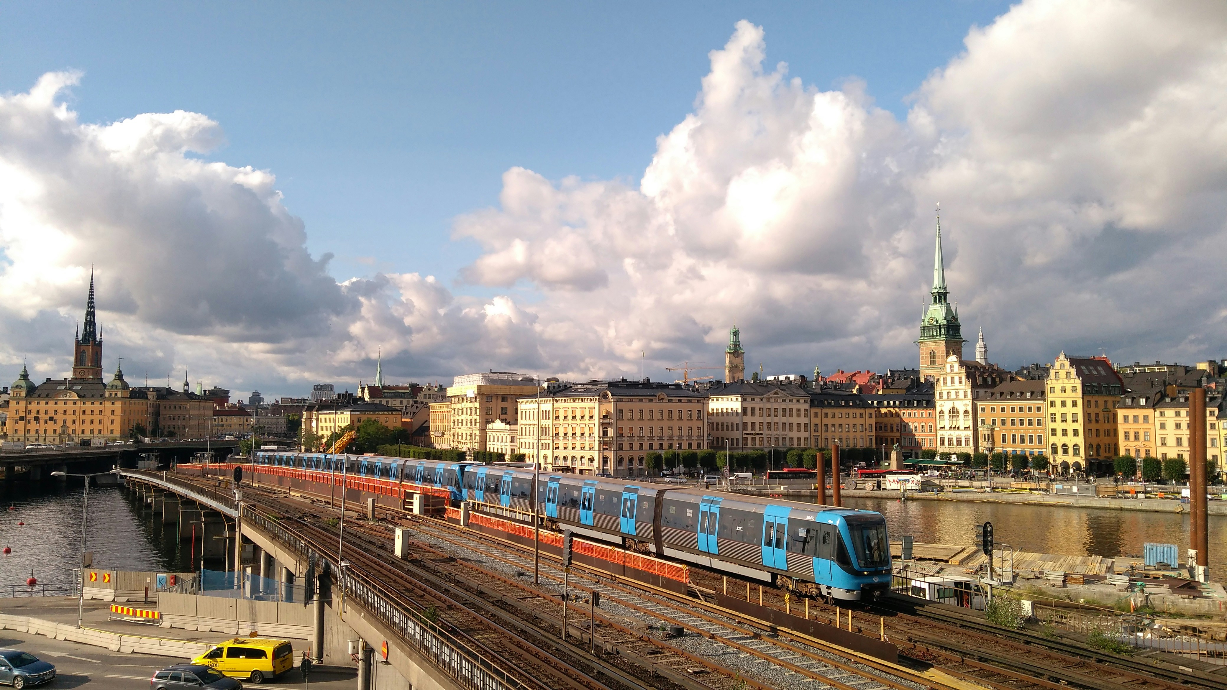 Blue commuter train glides along a sunlit urban riverfront