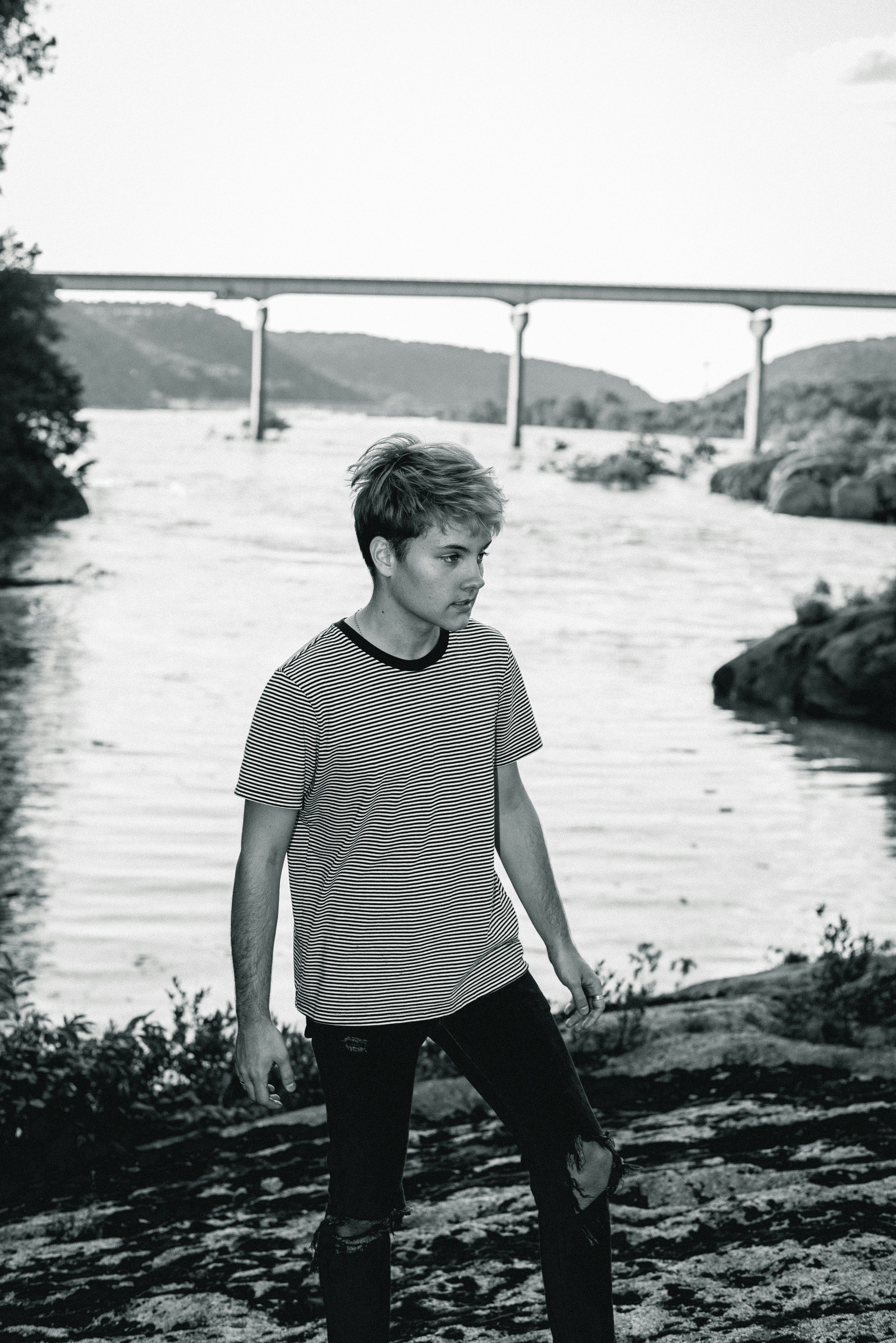 Quiet Contemplation by the Shore: A Striped-Tee Teen and a Distant Bridge