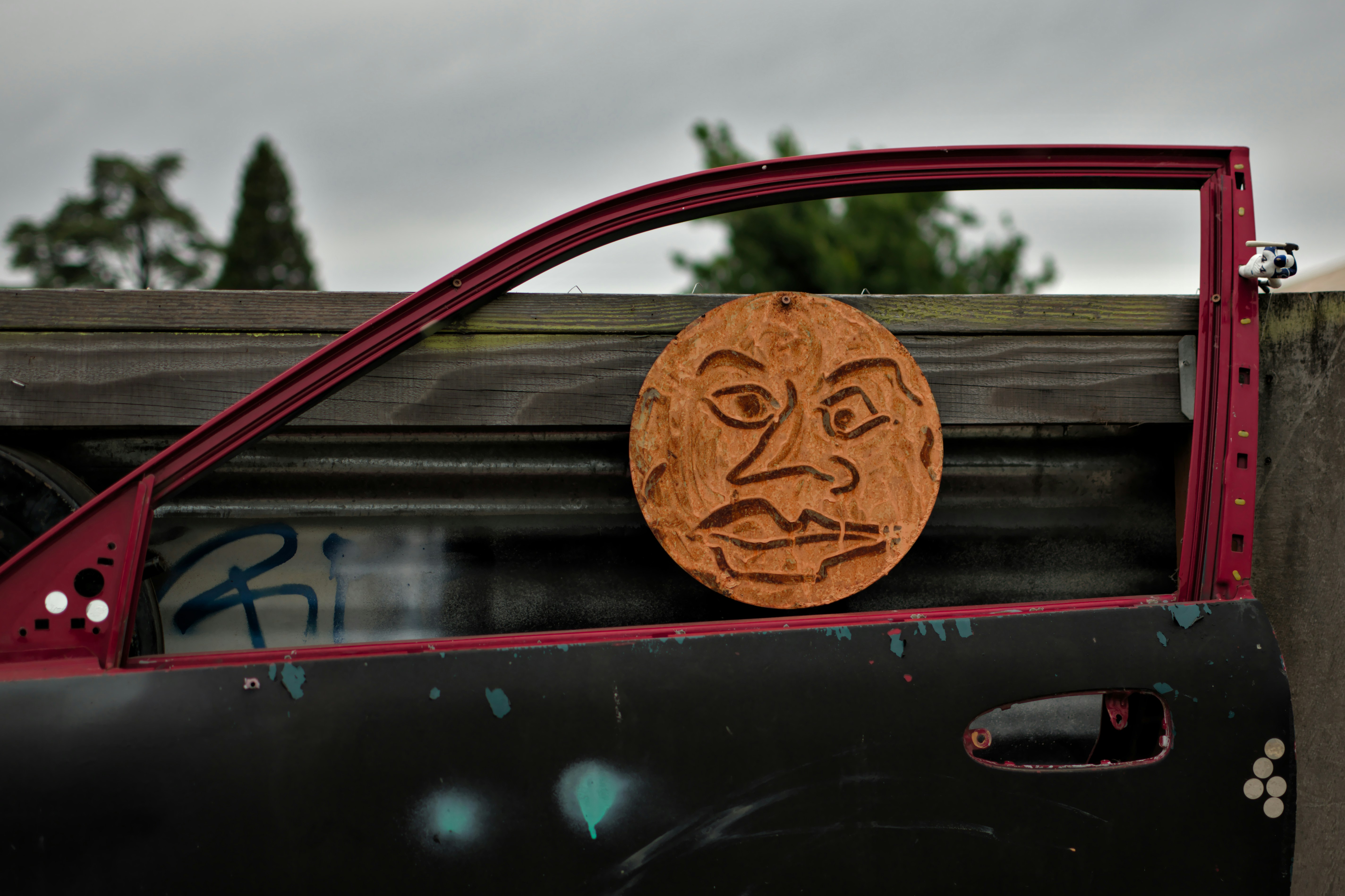 Circular Sun Face Anchored to a Graffiti-Clad Car Door