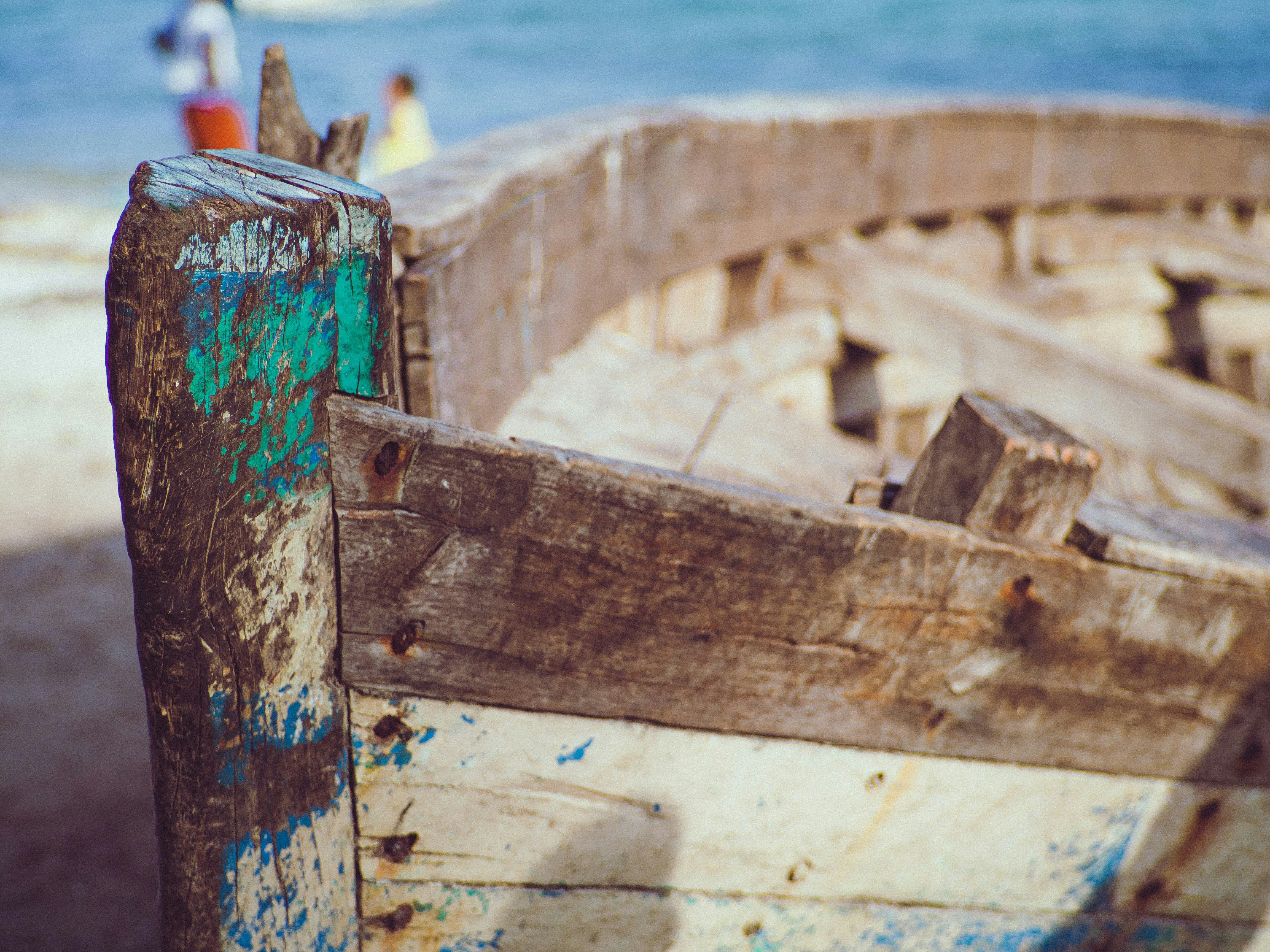 Close-up of an aged wooden boat resting on a sandy beach, with the ocean in the background.