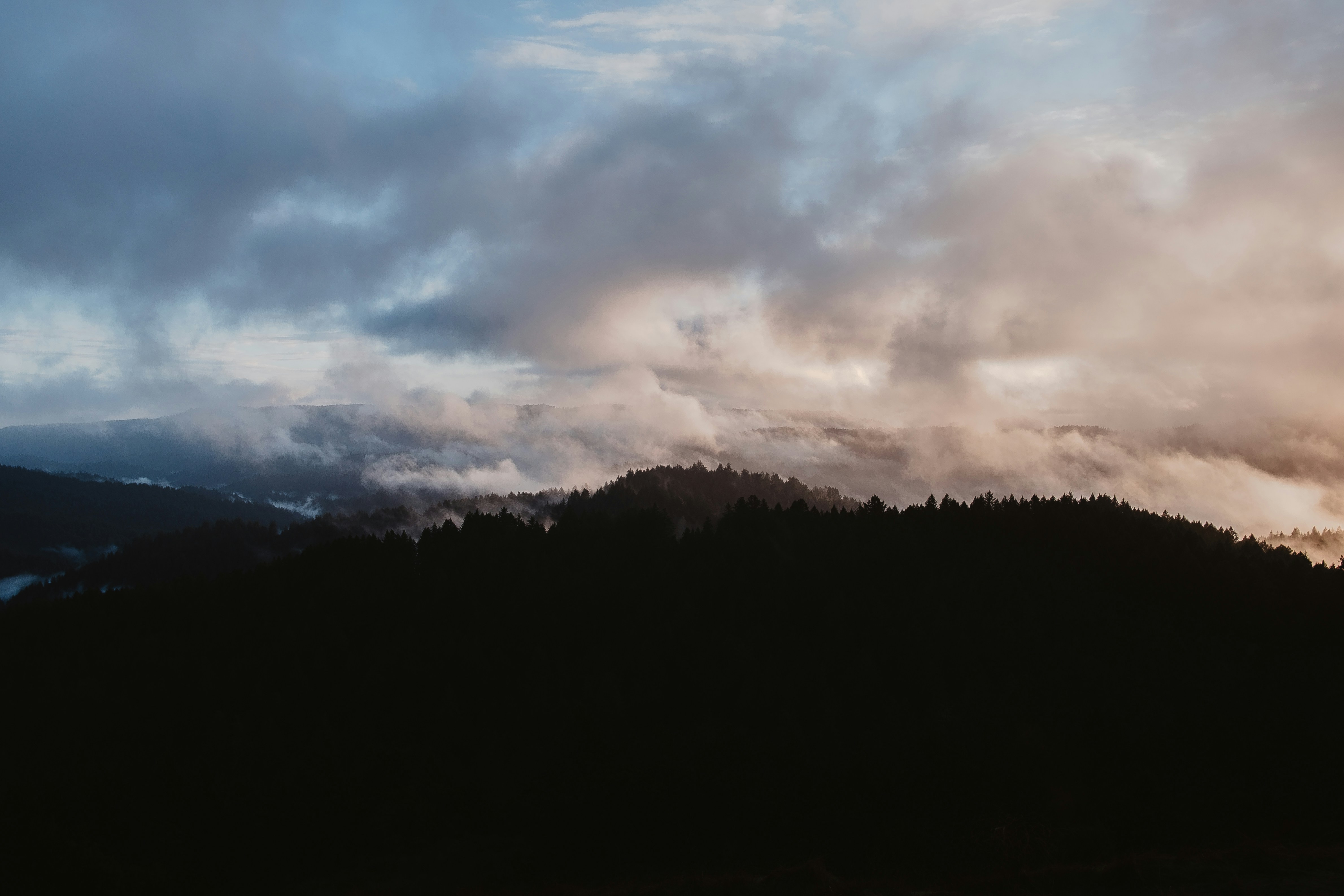 Silhouetted mountains beneath a sky transitioning from blue to fiery hues at dusk.