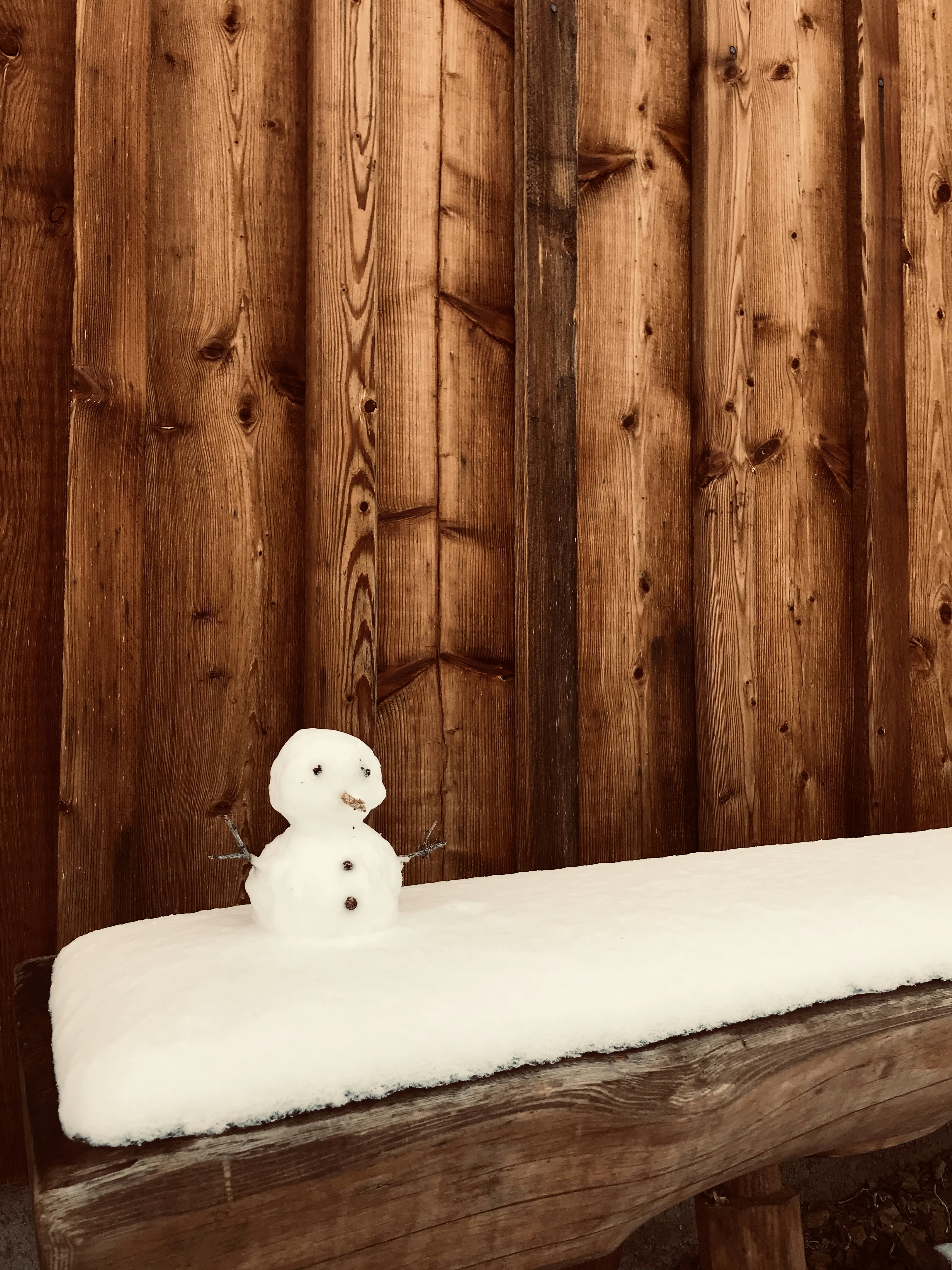 Tiny Snowman on a Snowy Bench Before Weathered Timber