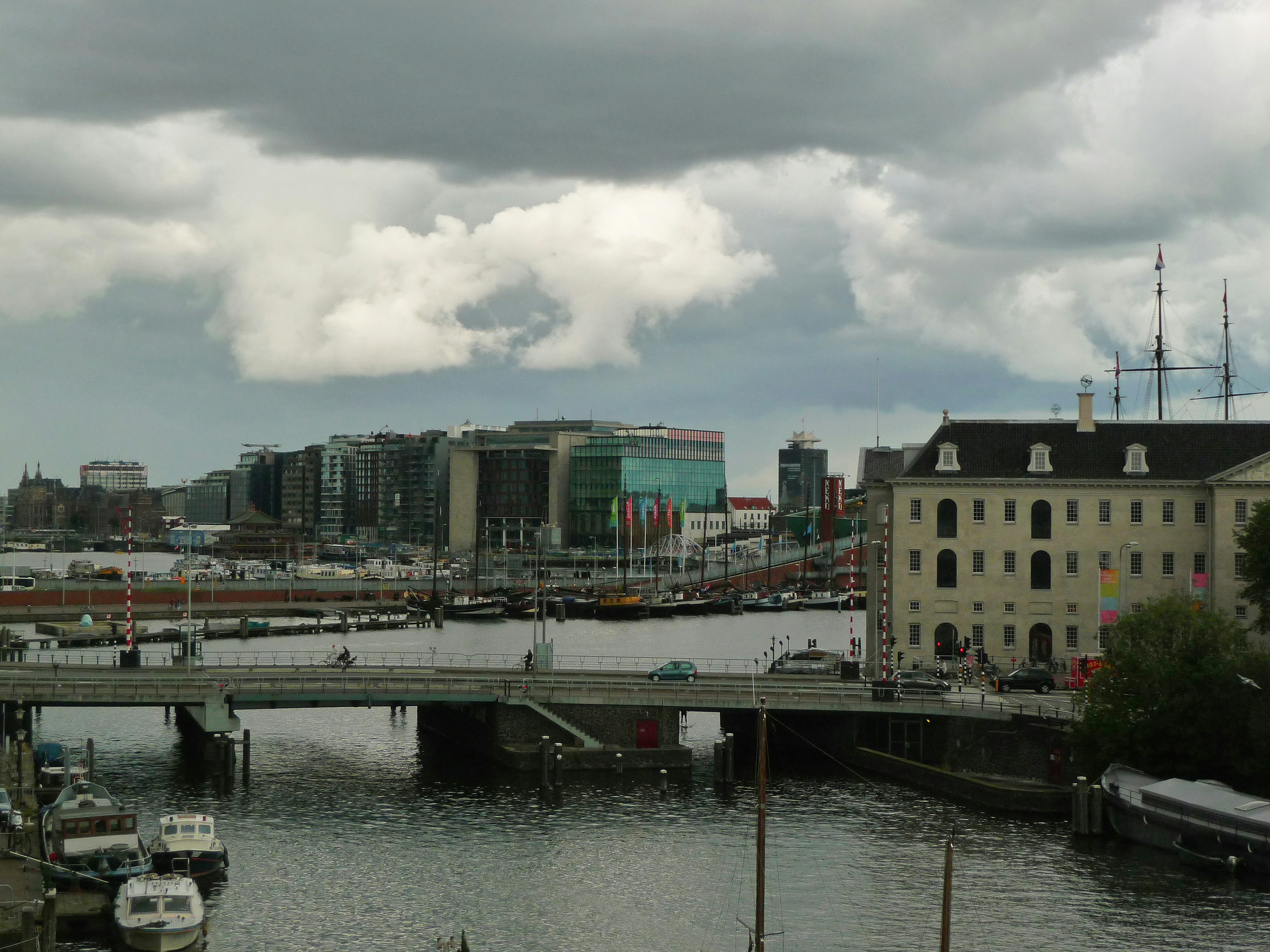 A bustling urban waterway featuring a bridge connecting contemporary architecture with historical buildings, under a dramatic sky.